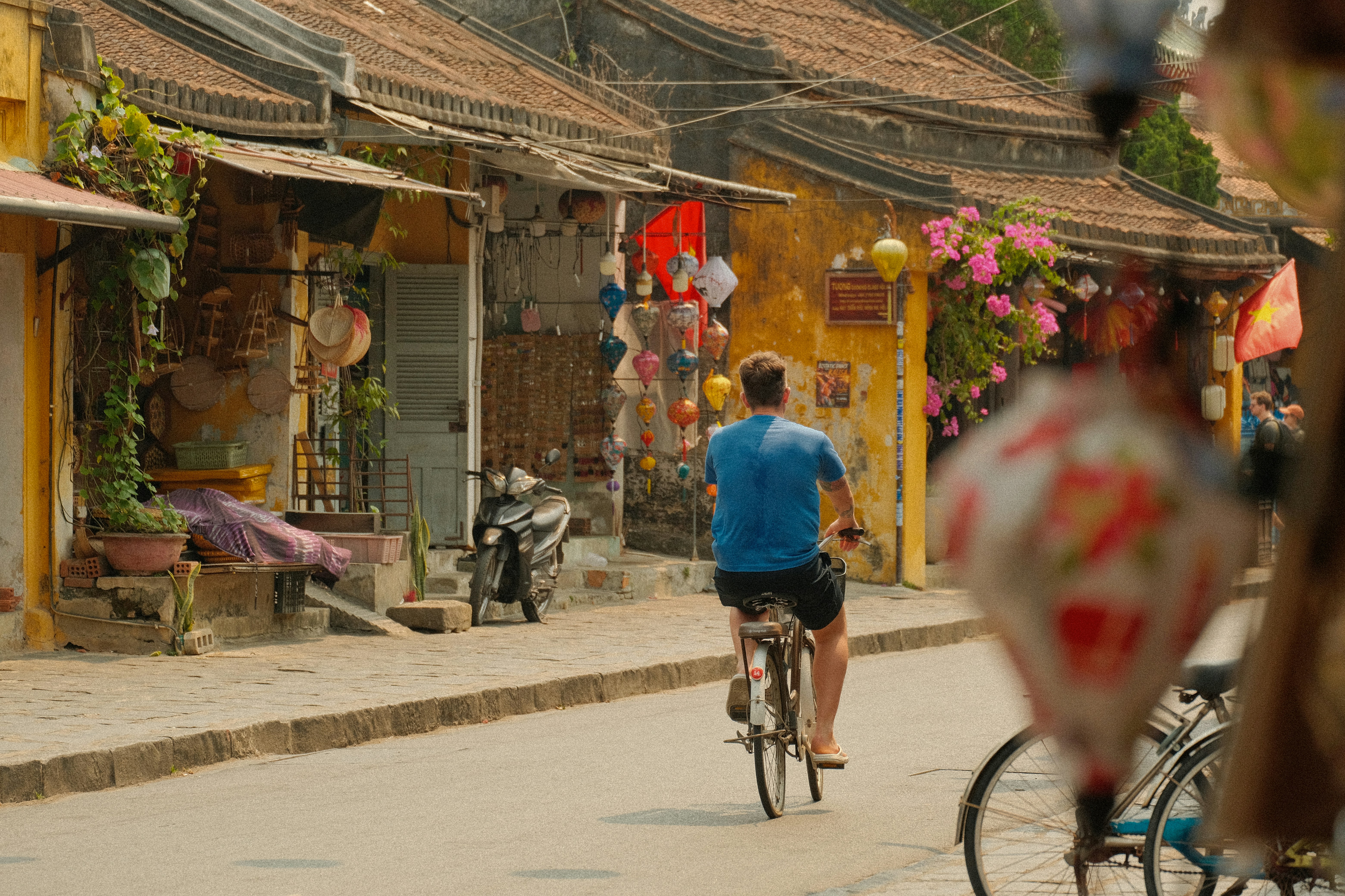 Cyclist Traverses a Sunlit Alley in a Colorful Asian Market