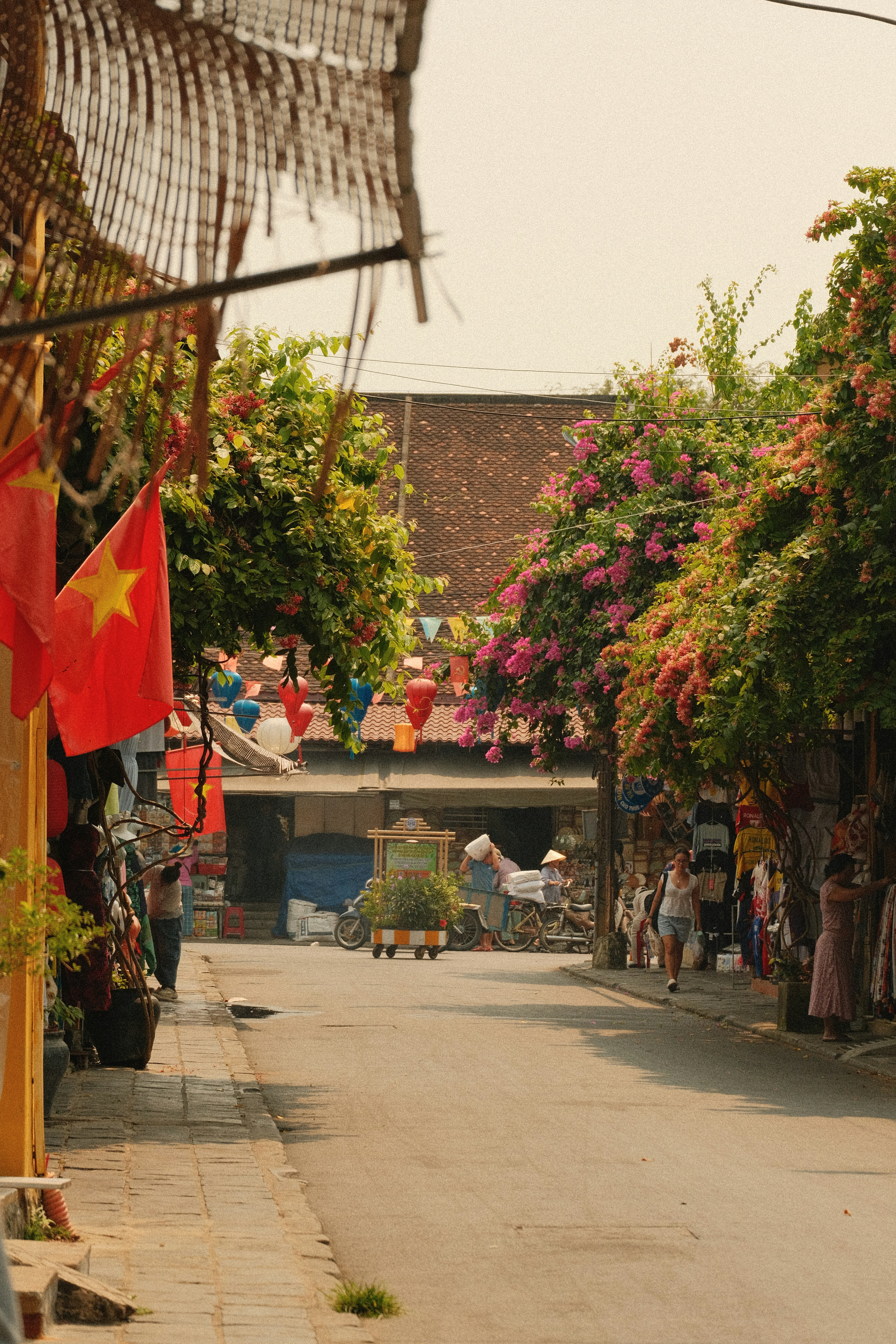 Sunlit Street Bazaar: Lanterns, Flags, and Blossoms Along a Quiet Vietnamese Lane