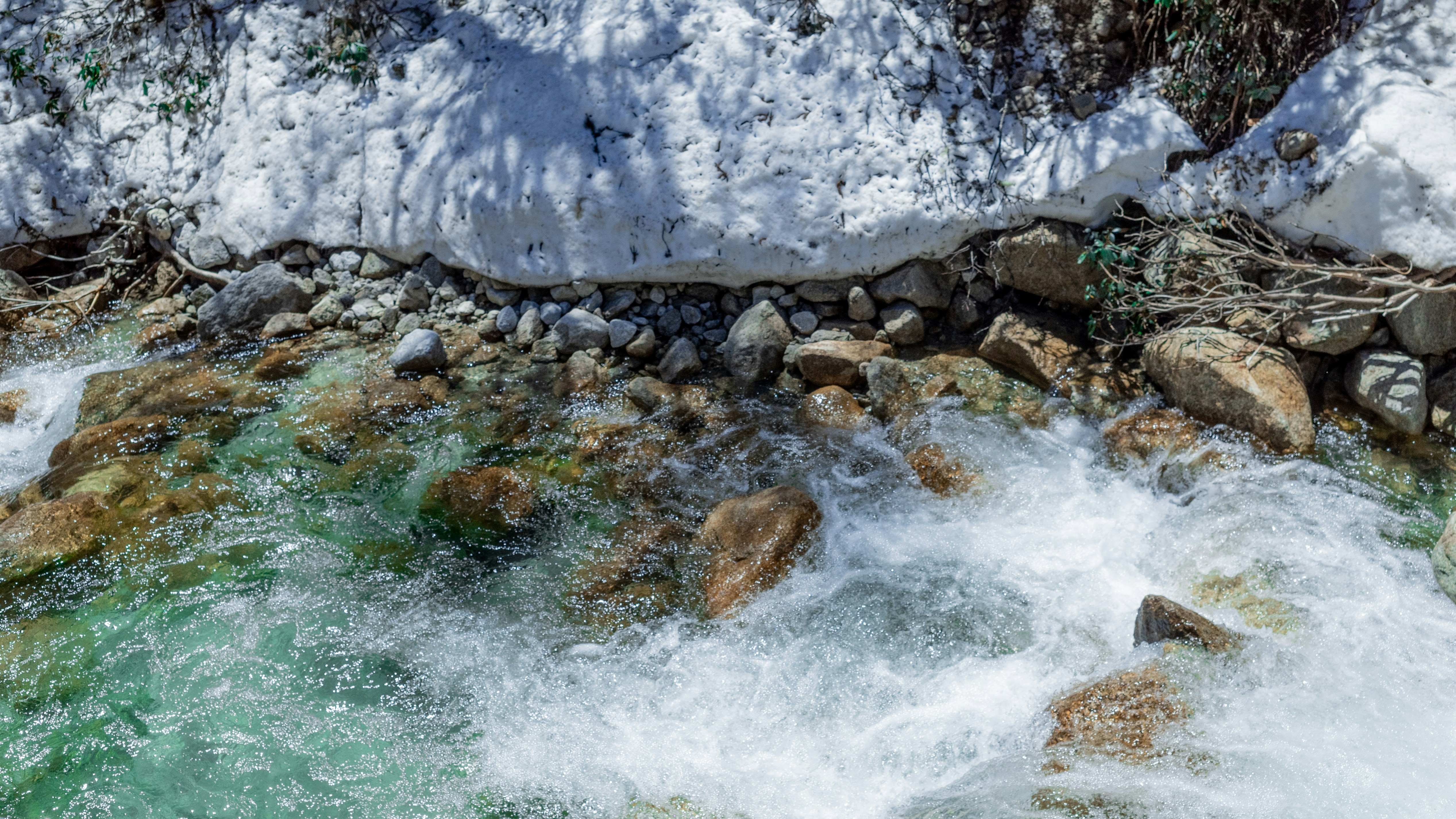 Crystal Cascade: Green Stream Washes Over Stones Under Snow Rim