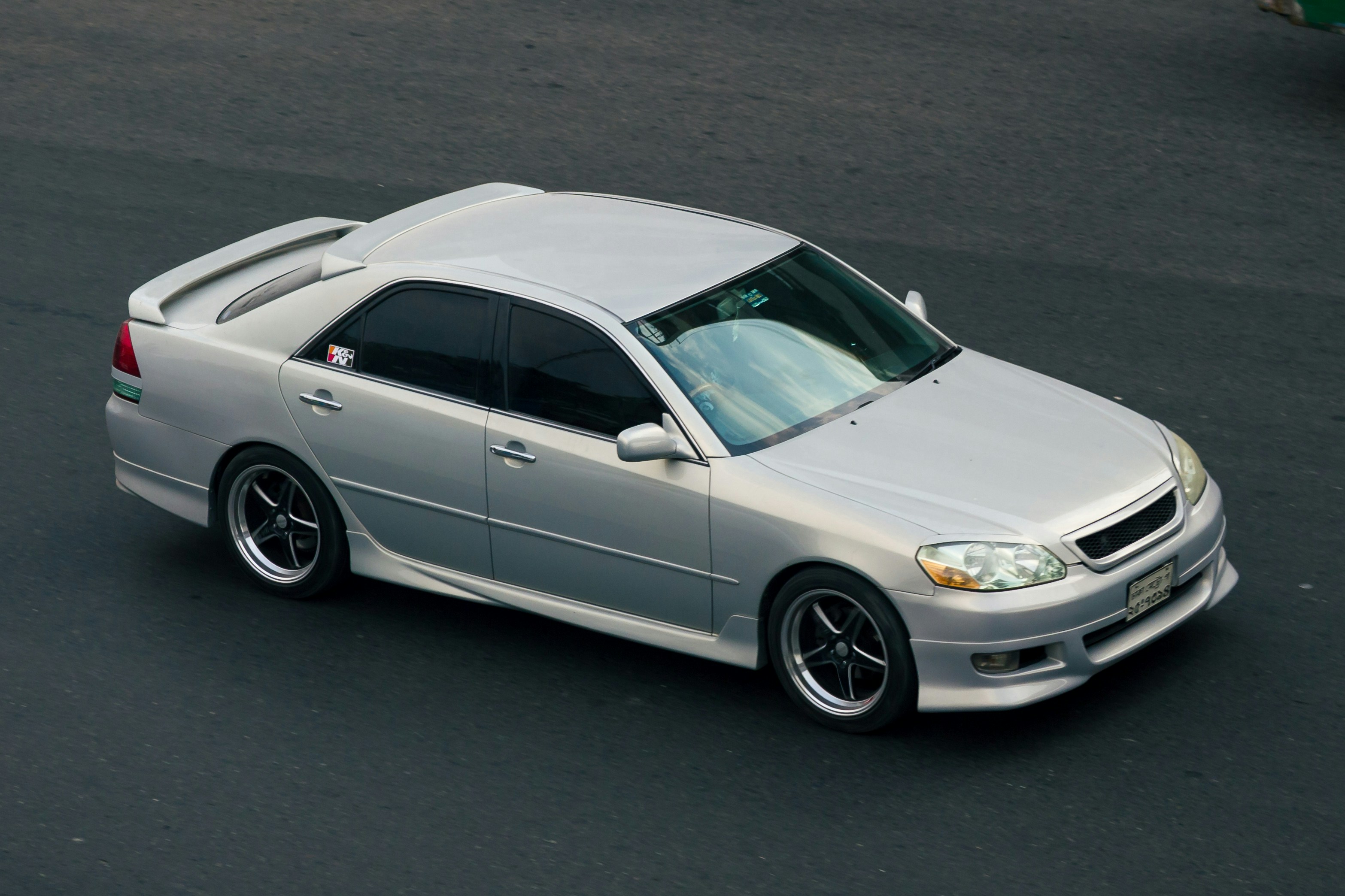 Silver sedan, aerial view with sunlit curves and spoiler