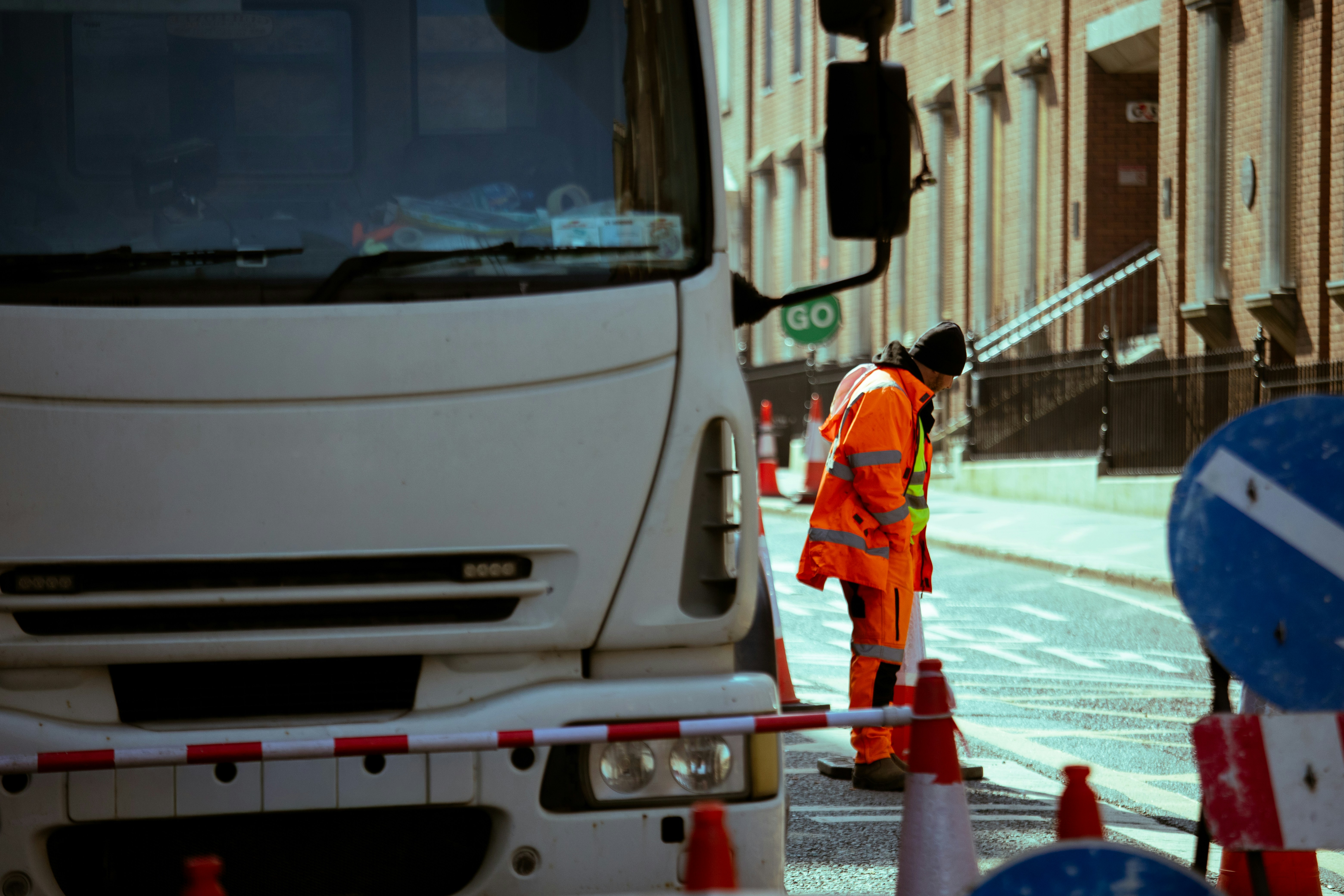 Orange safety gear amidst a roadwork tableau beside a stationary bus