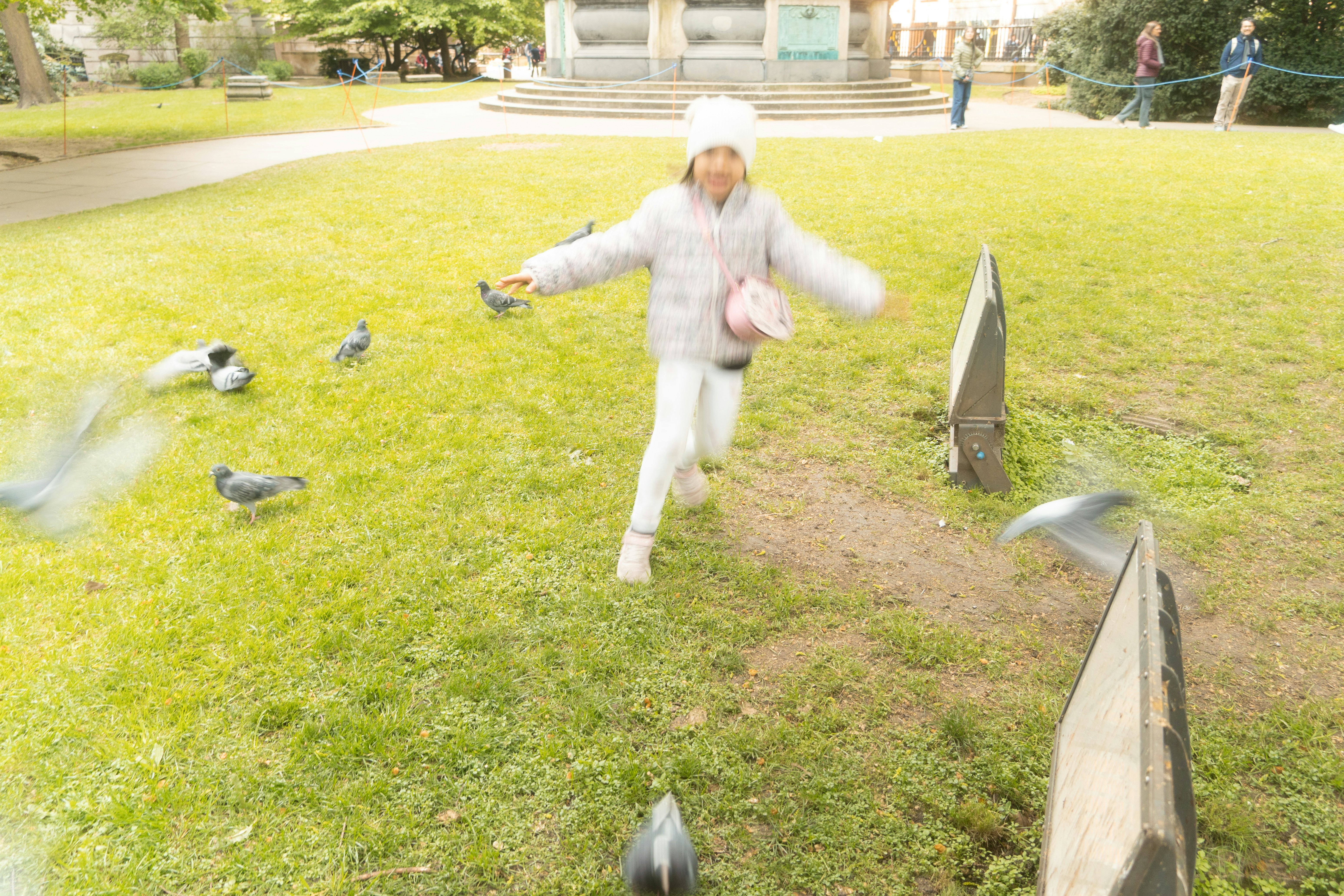 Child in motion near a park railing as pigeons scatter