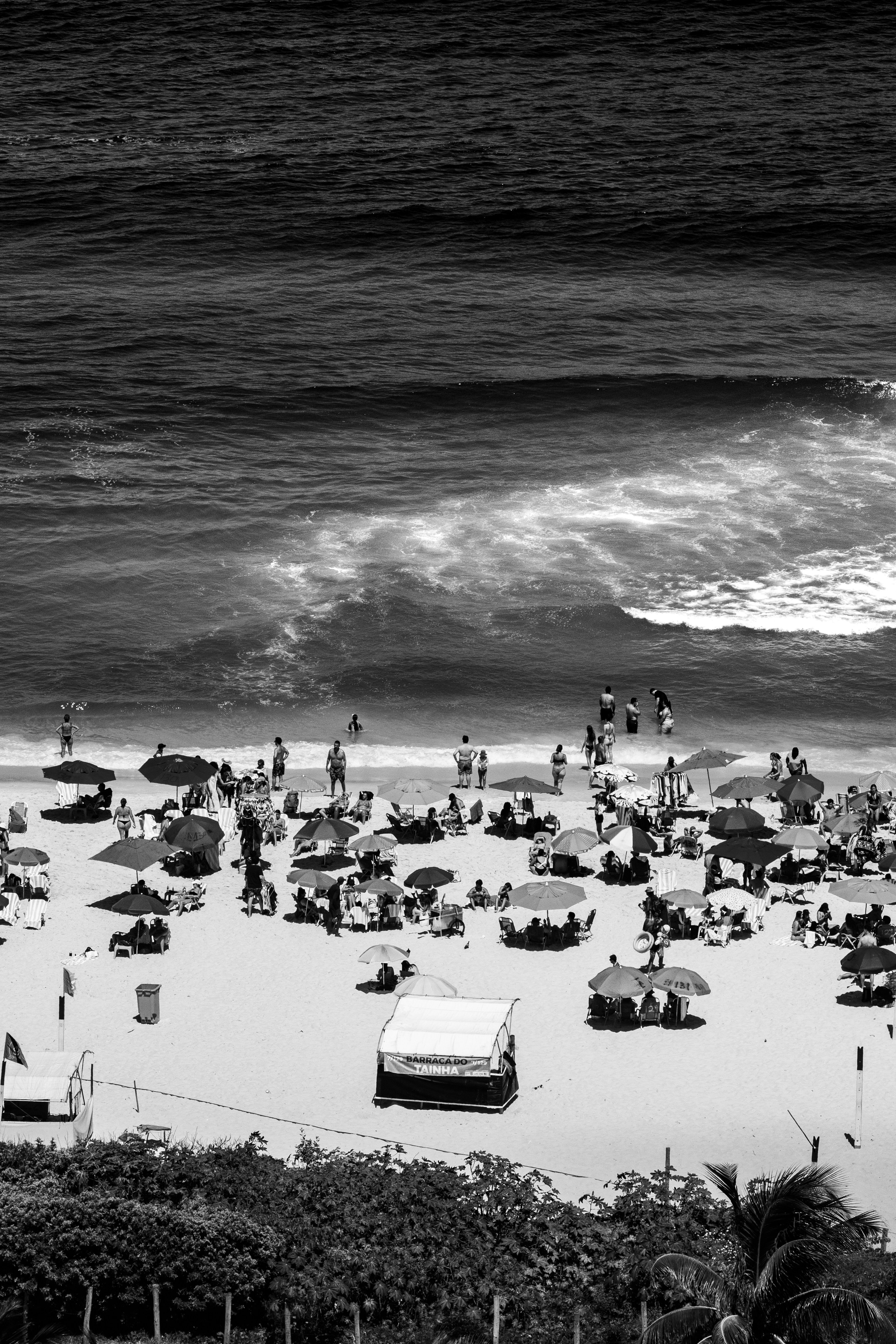 Sunlit shoreline in monochrome: beachgoers and surf at low tide