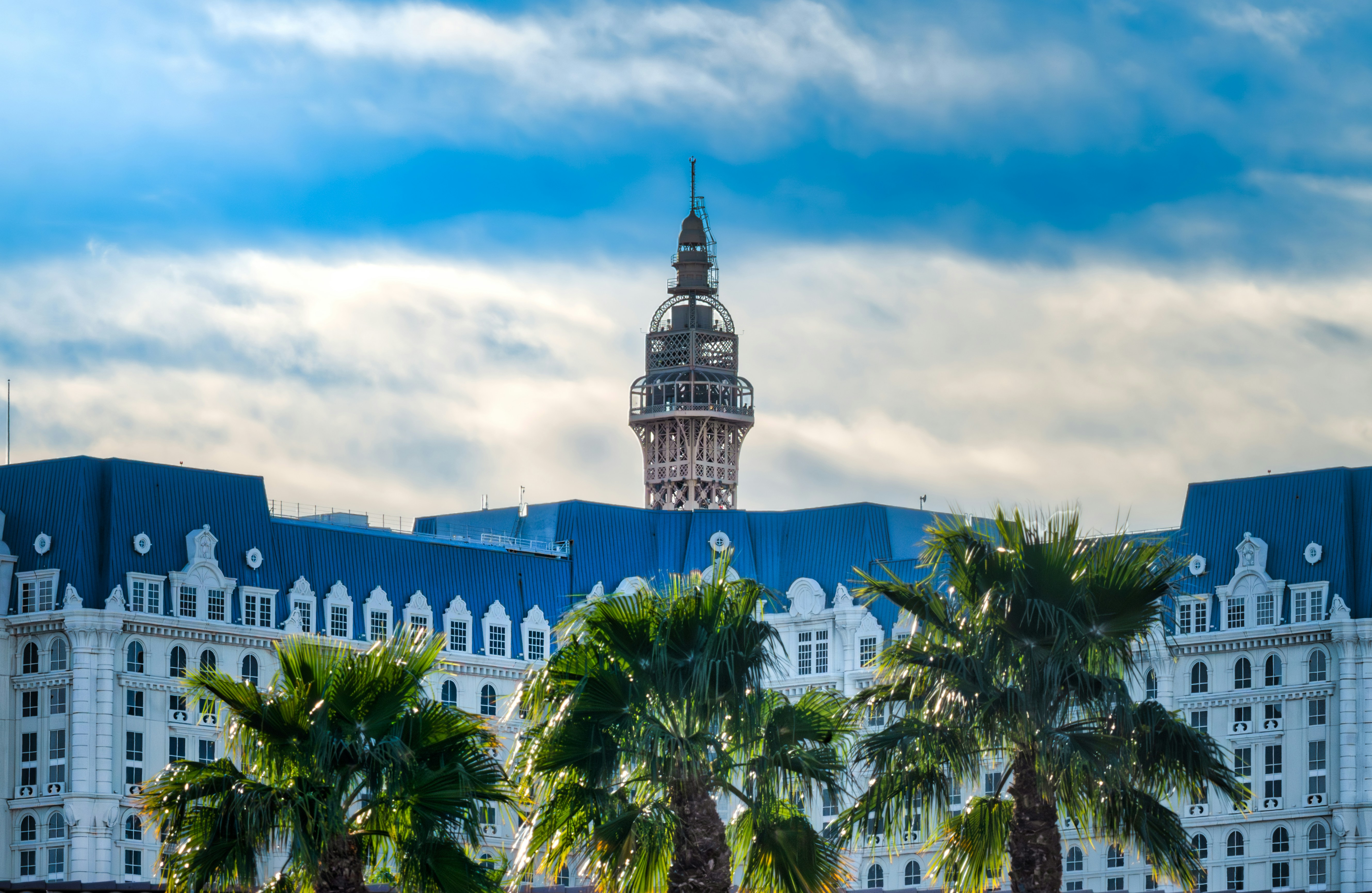 Blue-Hued Facade and Towerline Above Palm-Lined Plaza