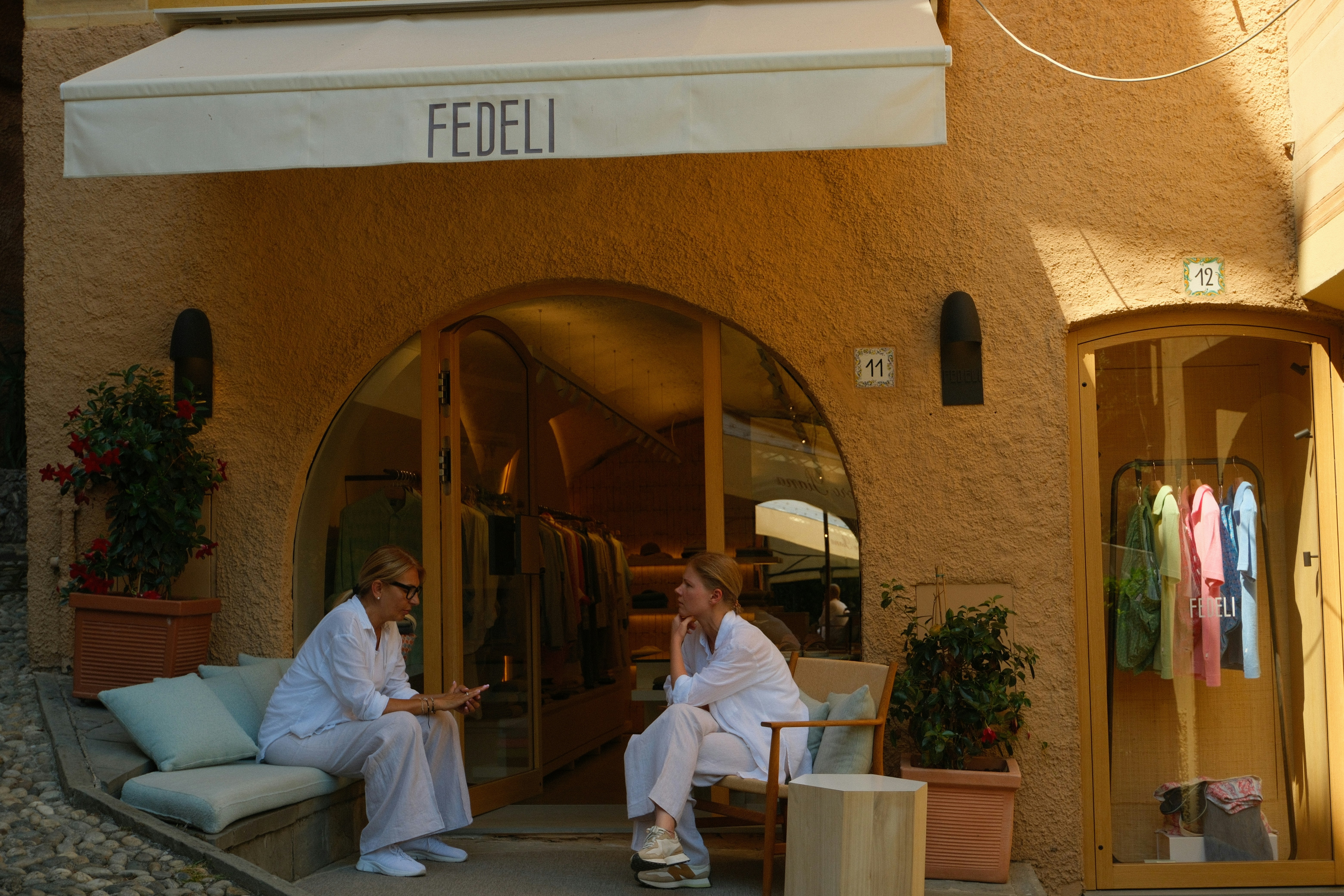 Two white-clad companions converse on a sunlit Mediterranean doorway
