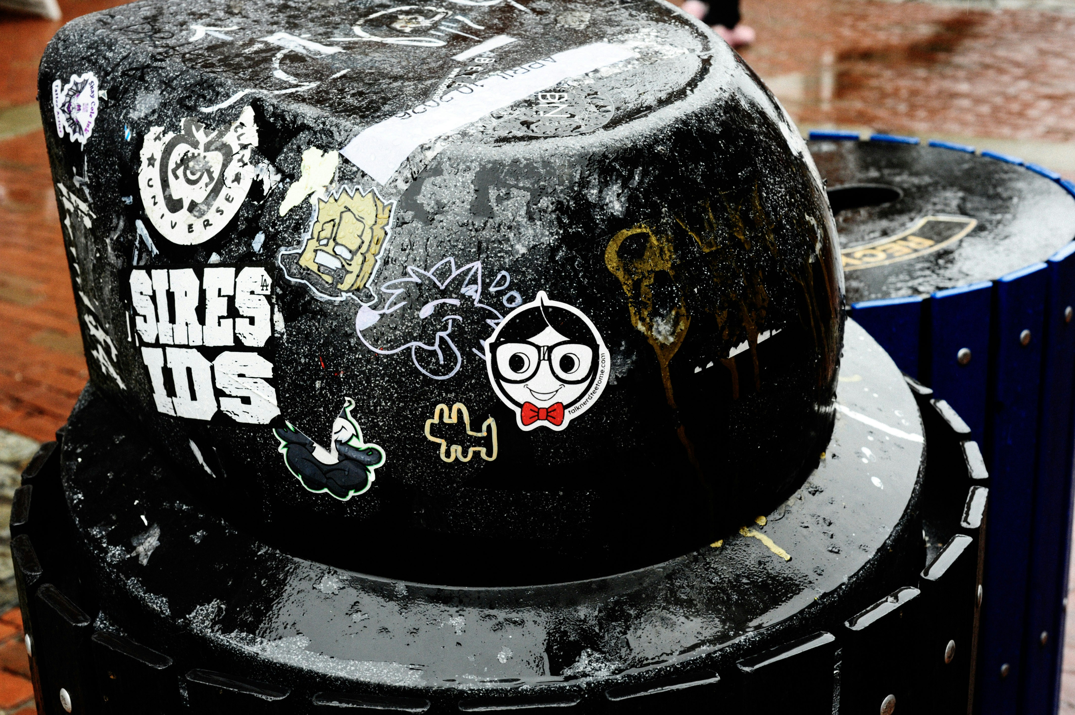 Stickered trash can with doodles and graffiti at a playground