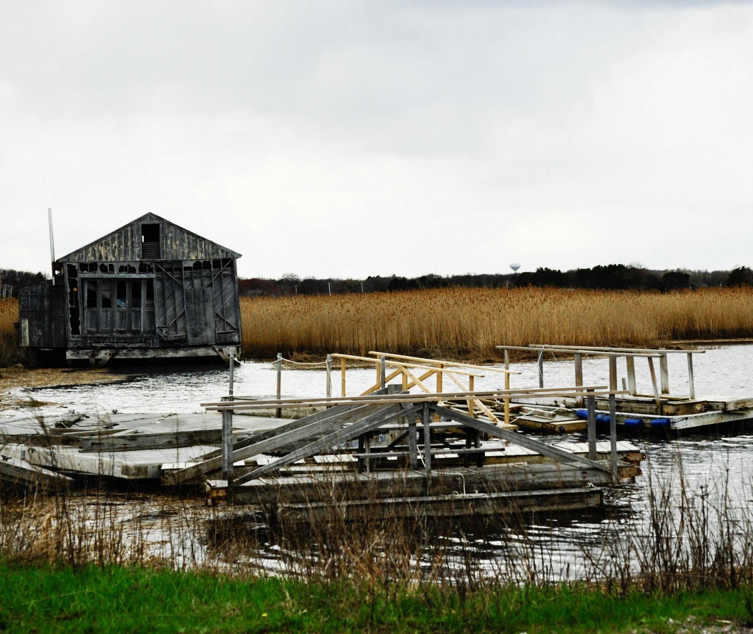 Weathered boathouse on a marshy inlet under a pale sky