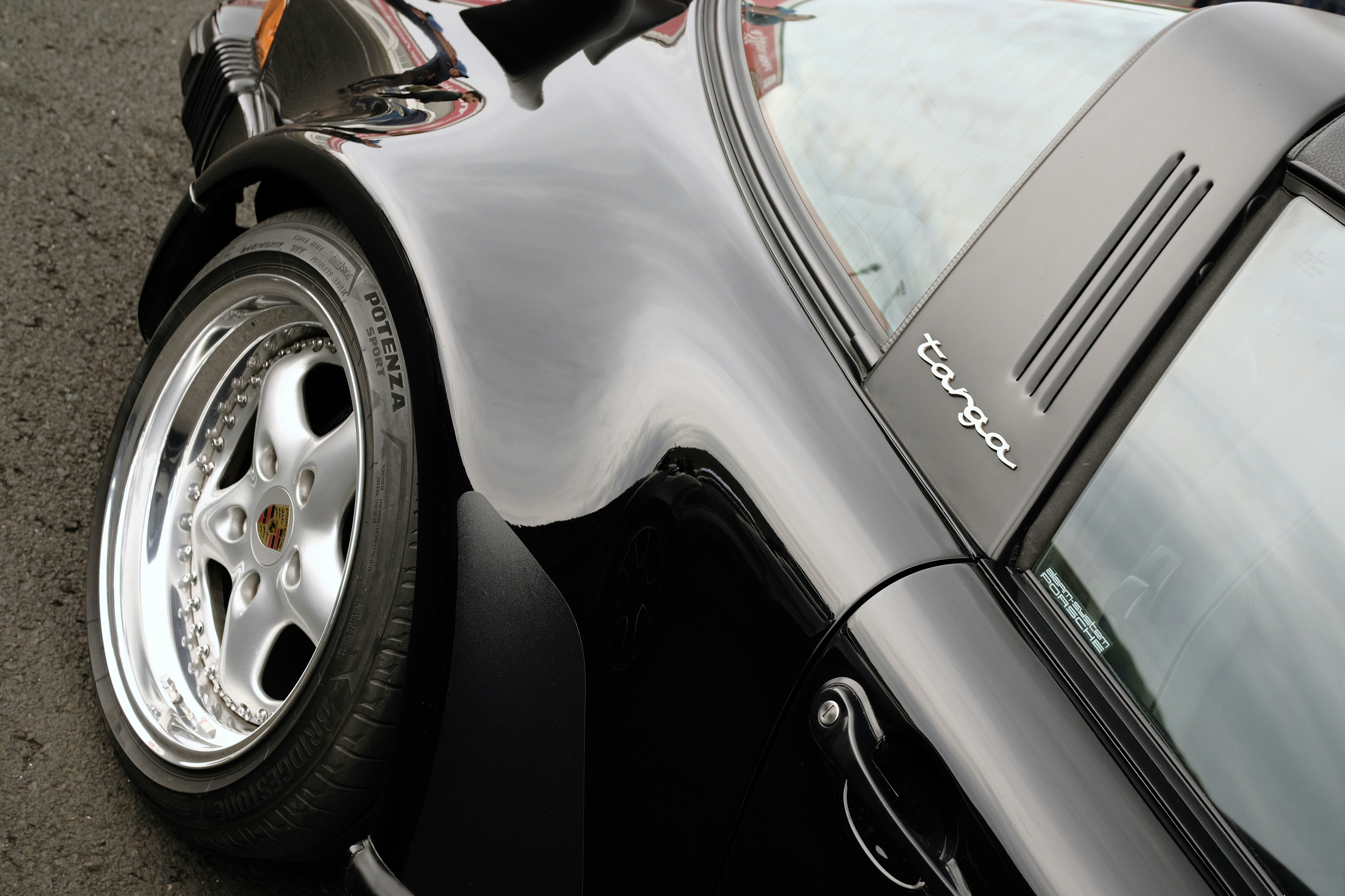 Glossy Porsche silhouette: near-side front wheel and badge on a curved fender