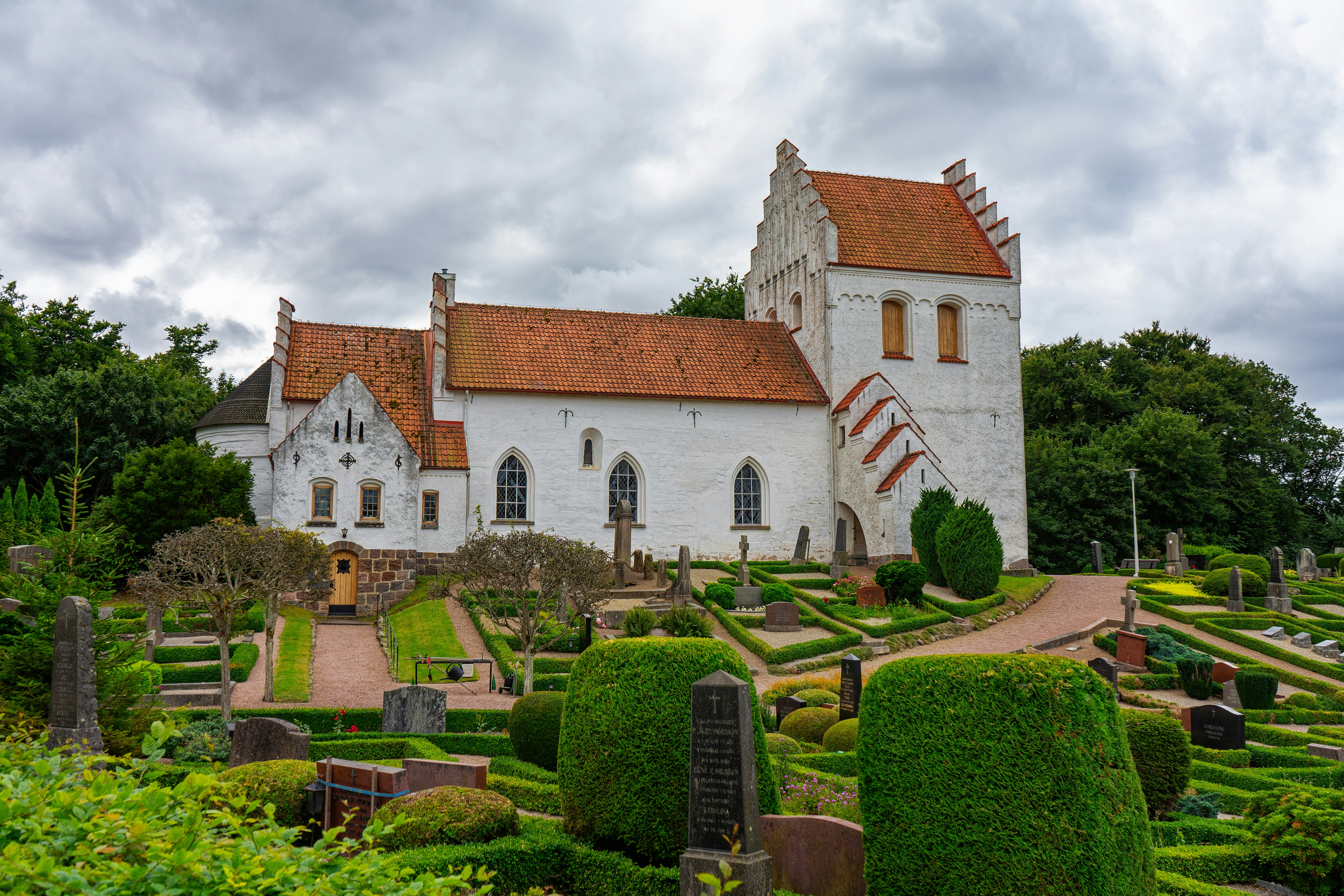 White-walled church amid sculpted hedges and graves