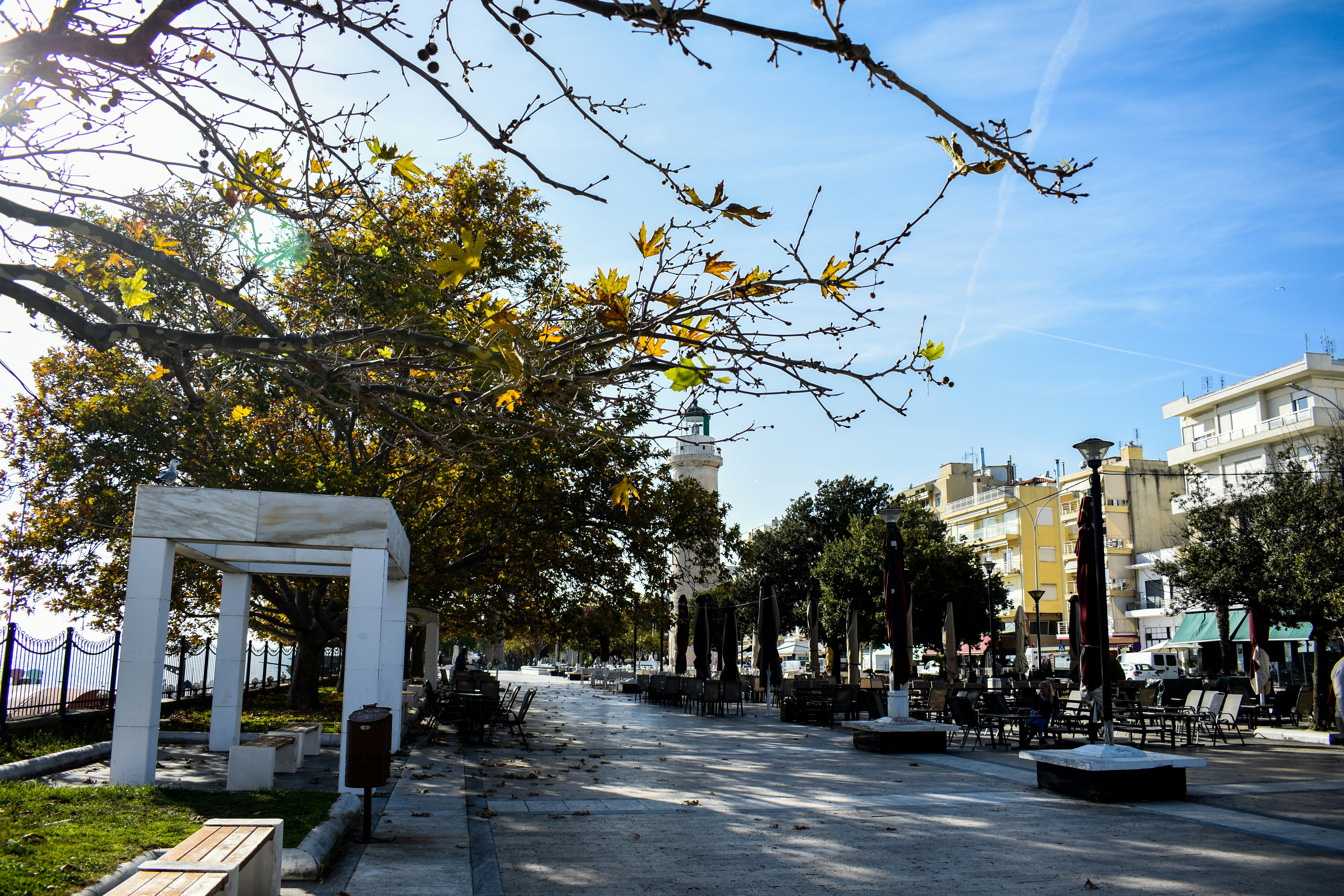 Promenade in the Coastal Town: Sunlit Trees, Waterfront Arches, and Lounging Patrons