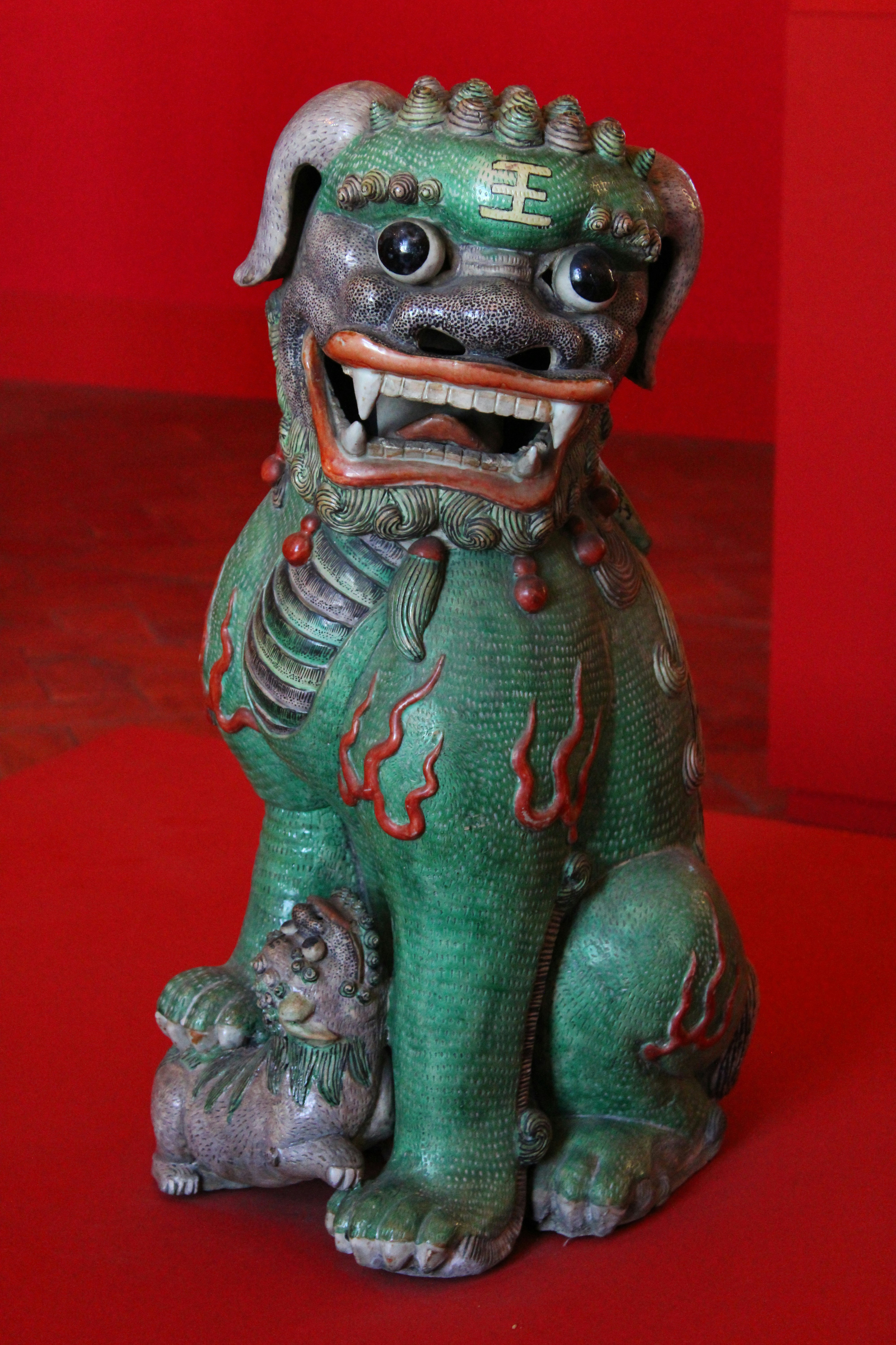 Green Guardian with Tiny Companion: A Ceremonial Statue Foregrounded in Red