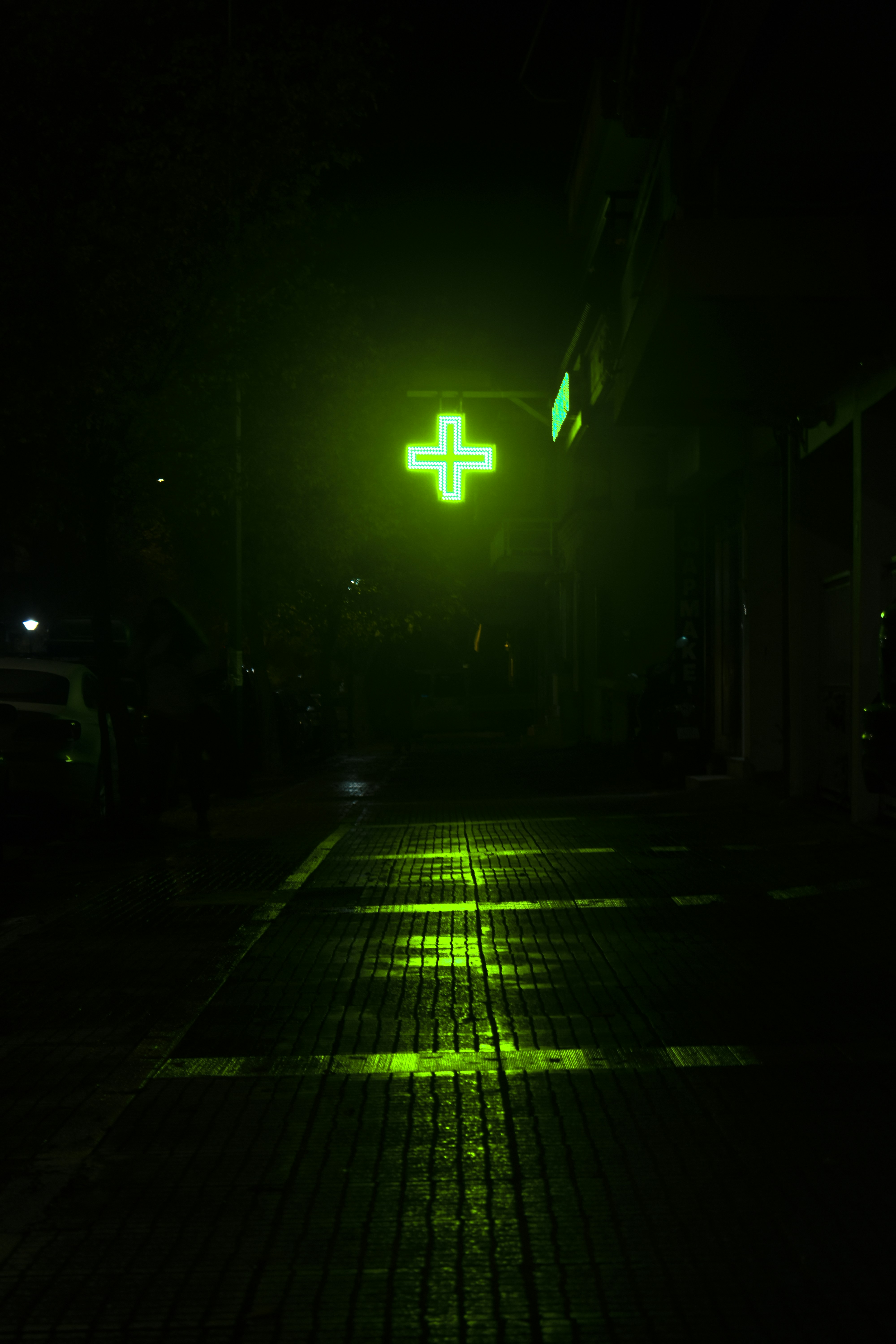 Neon Green Cross: Night Pharmacy Sign Over a Reflective Wet Street