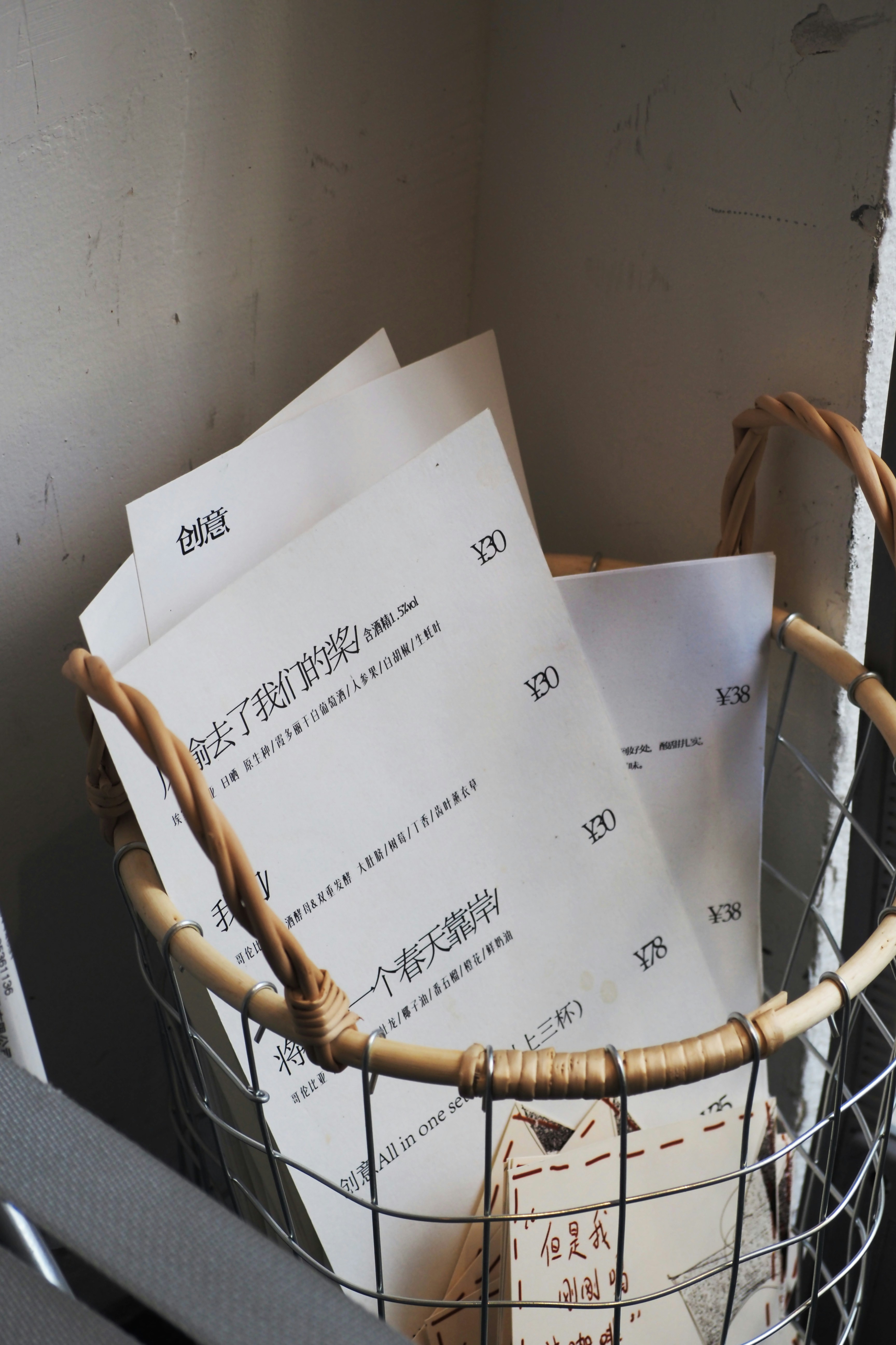 White papers with text in a basket against a wall; a simple still life with a casual indoor setting.