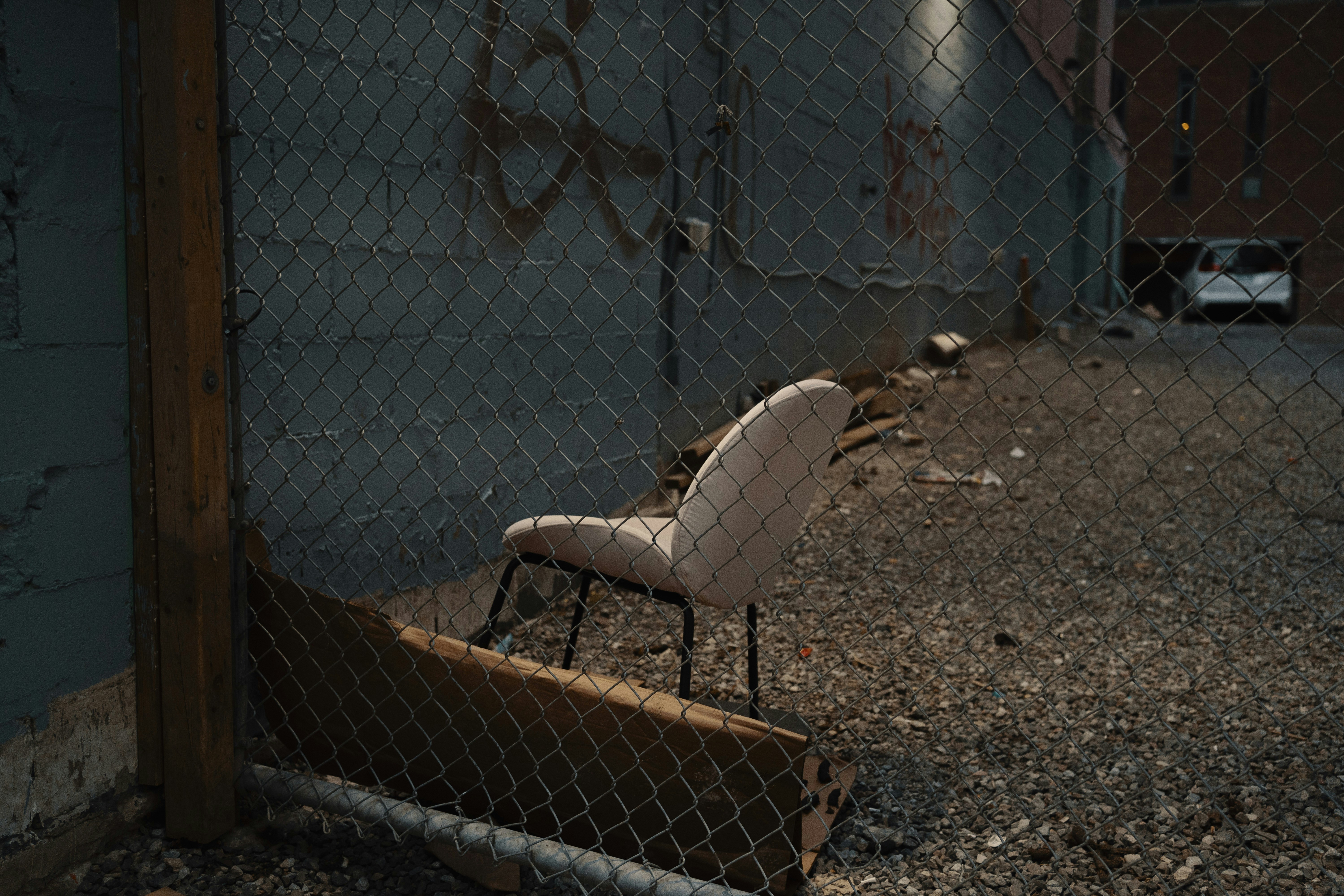 Abandoned chair near a chain-link boundary in a desolate lot