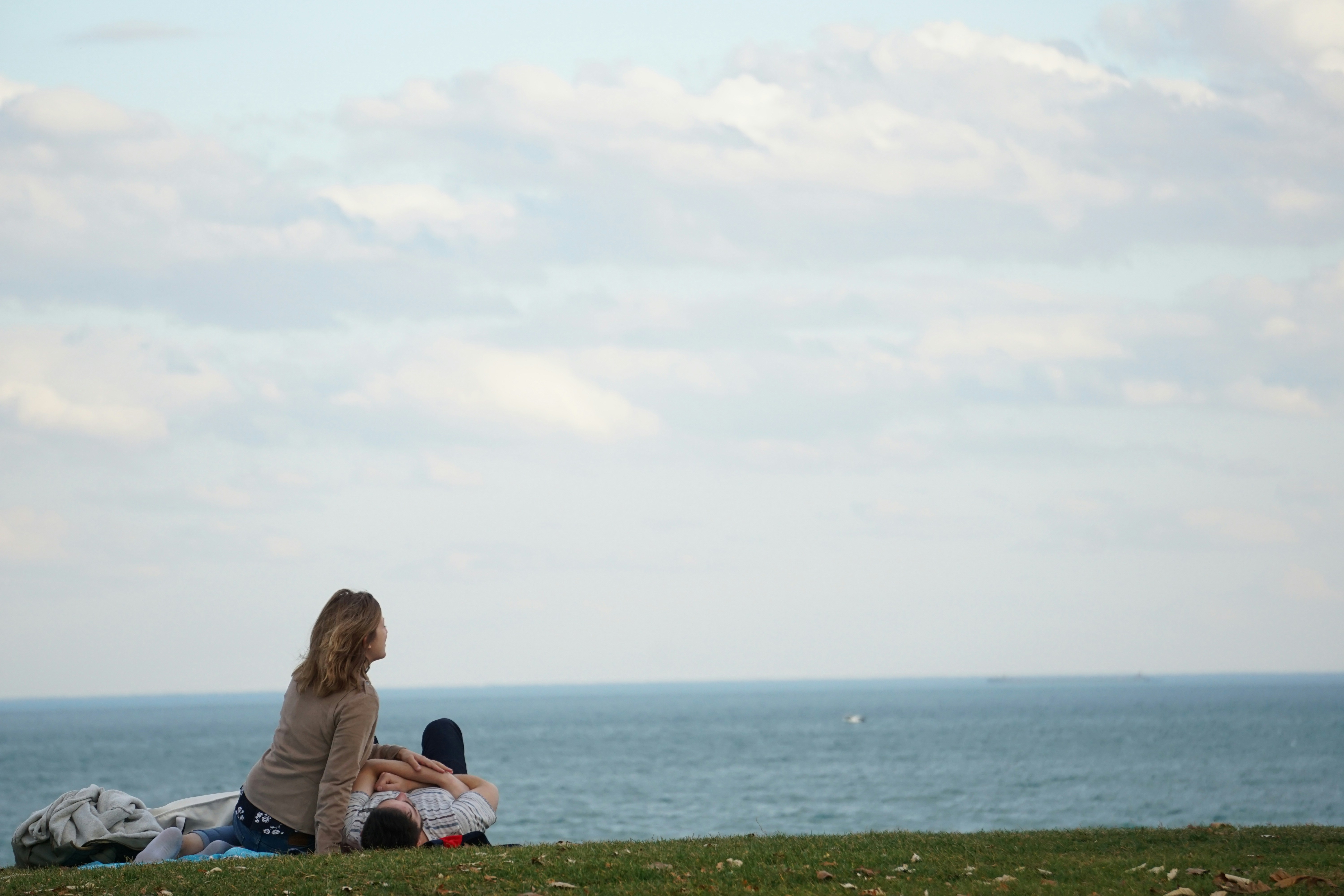 Quiet Coastline: A Woman and Child Rest on the Grass by the Sea