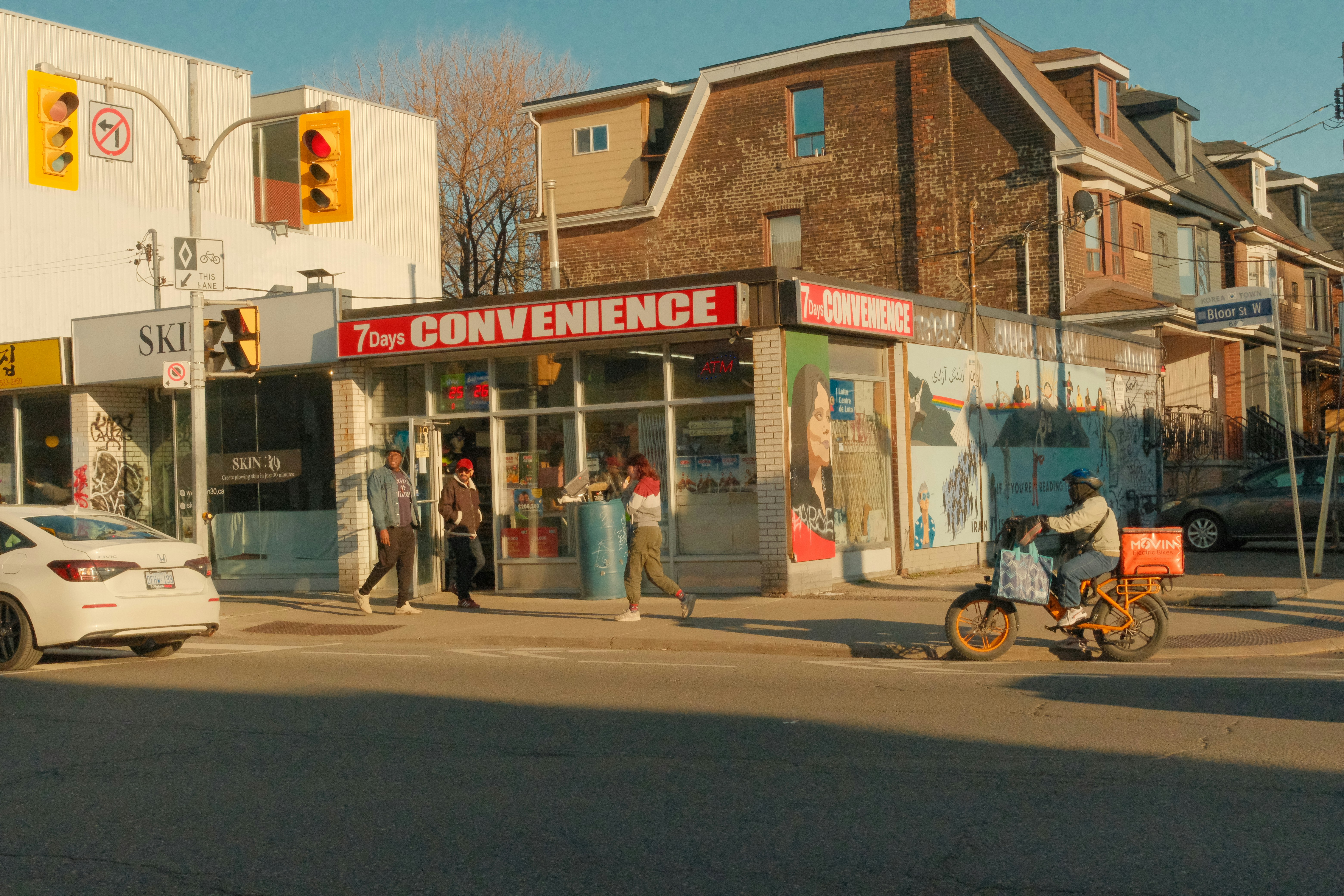Sunlit corner store and riders on a quiet urban afternoon