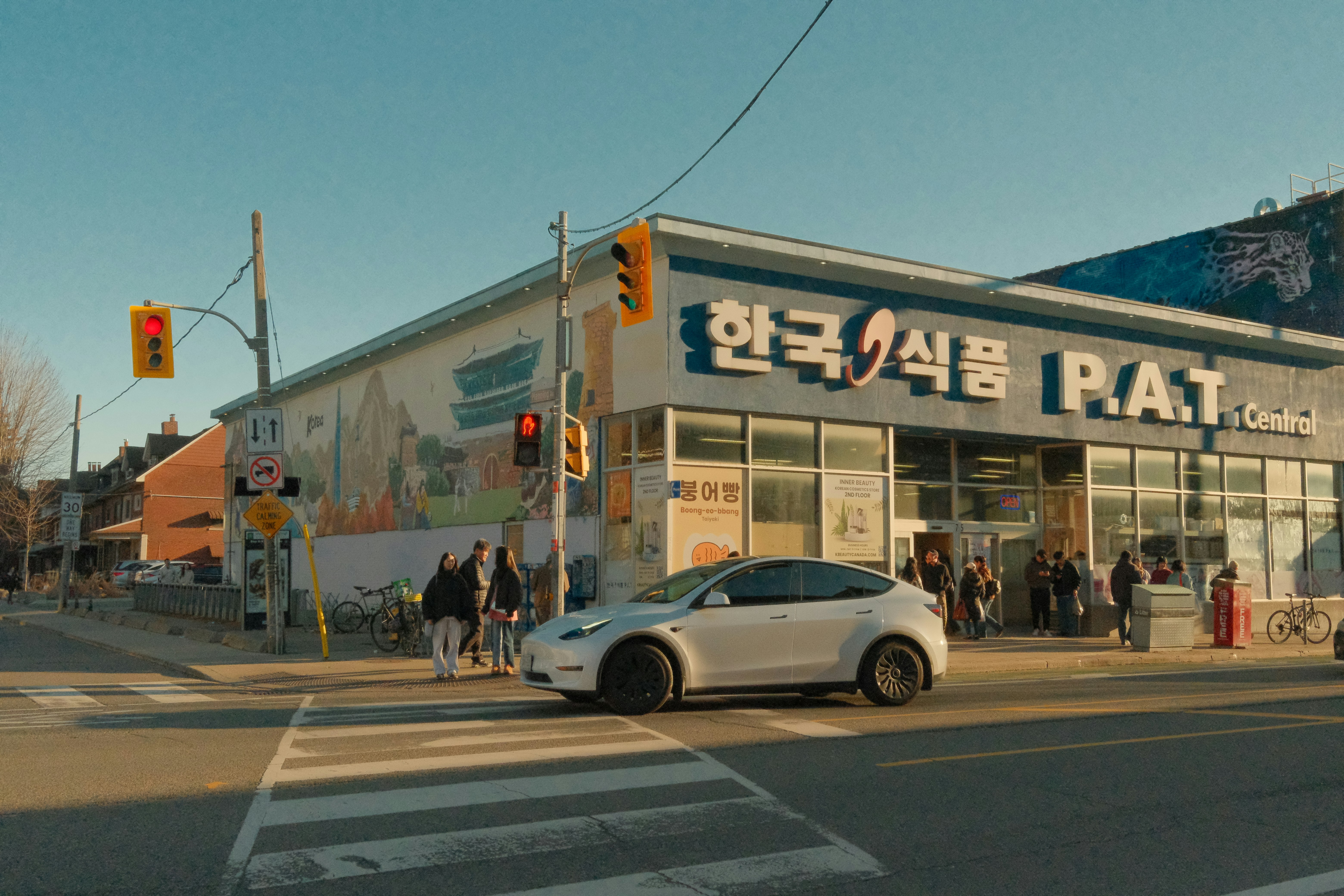 Crosswalk Moment: Silver Sedan Pauses Outside a Korean Market