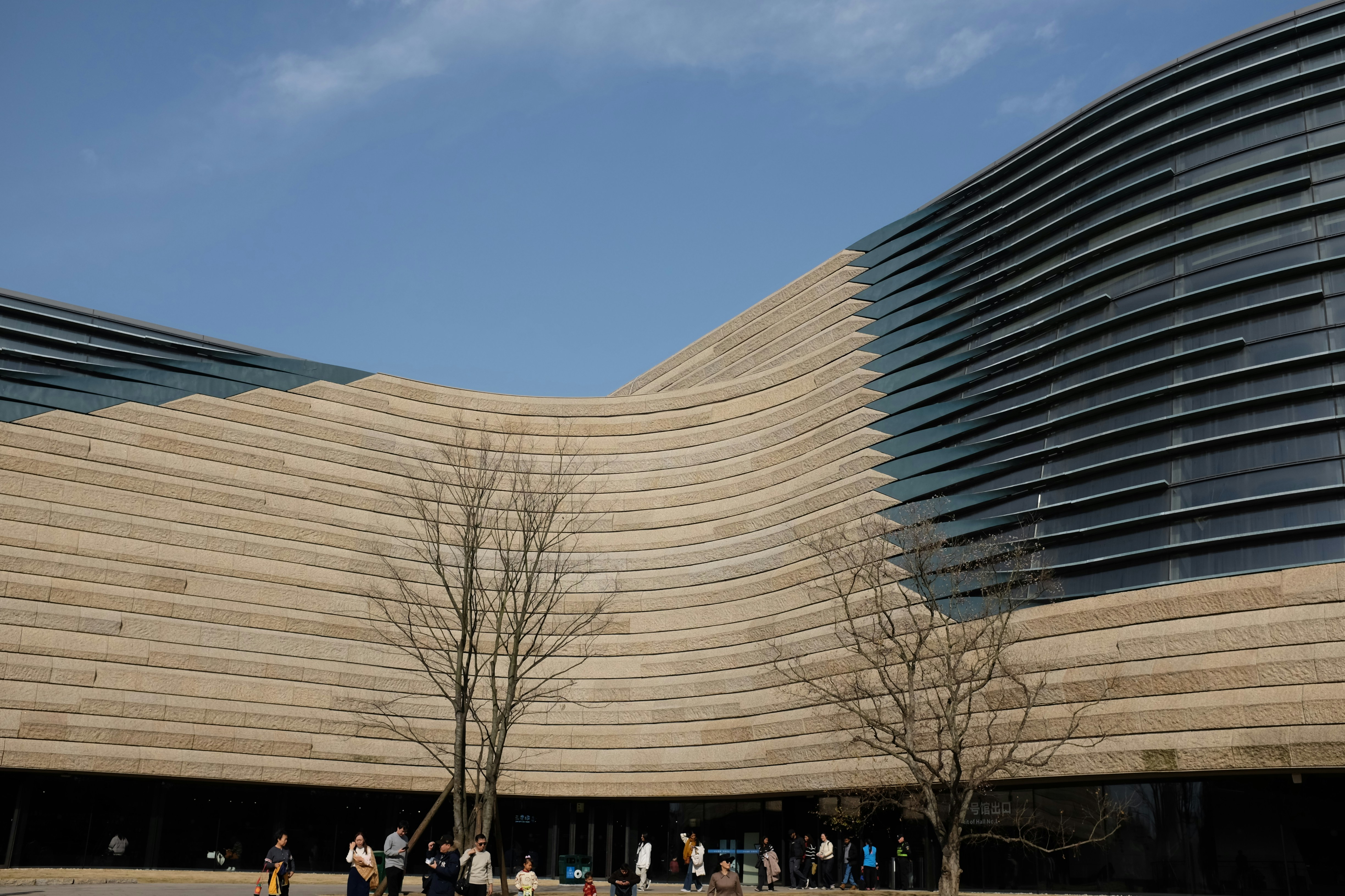 Curved sandstone walls frame a public plaza beneath a wavy architectural canopy