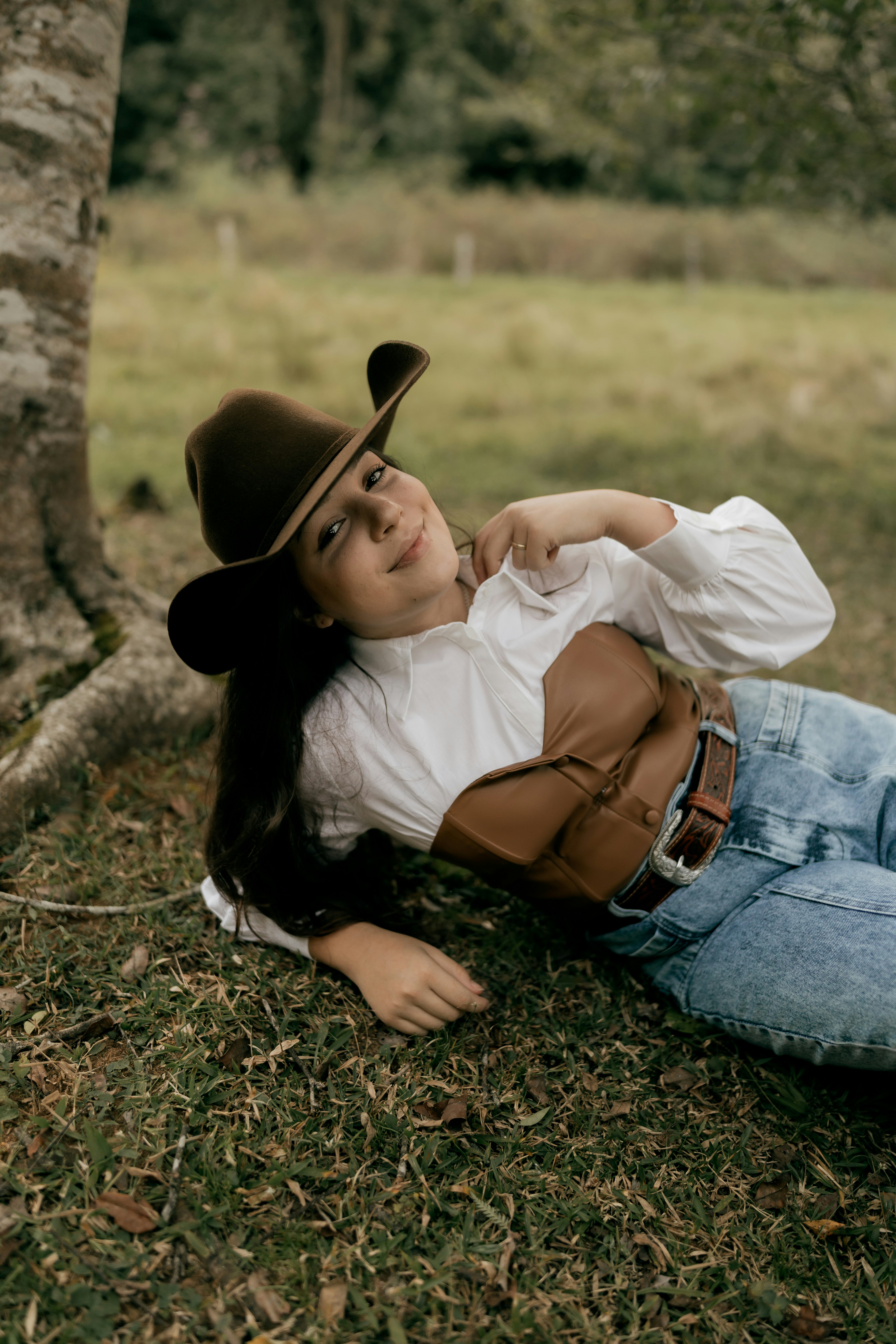 Cowgirl Relaxed: denim, white blouse, and a brown hat resting beneath a tree