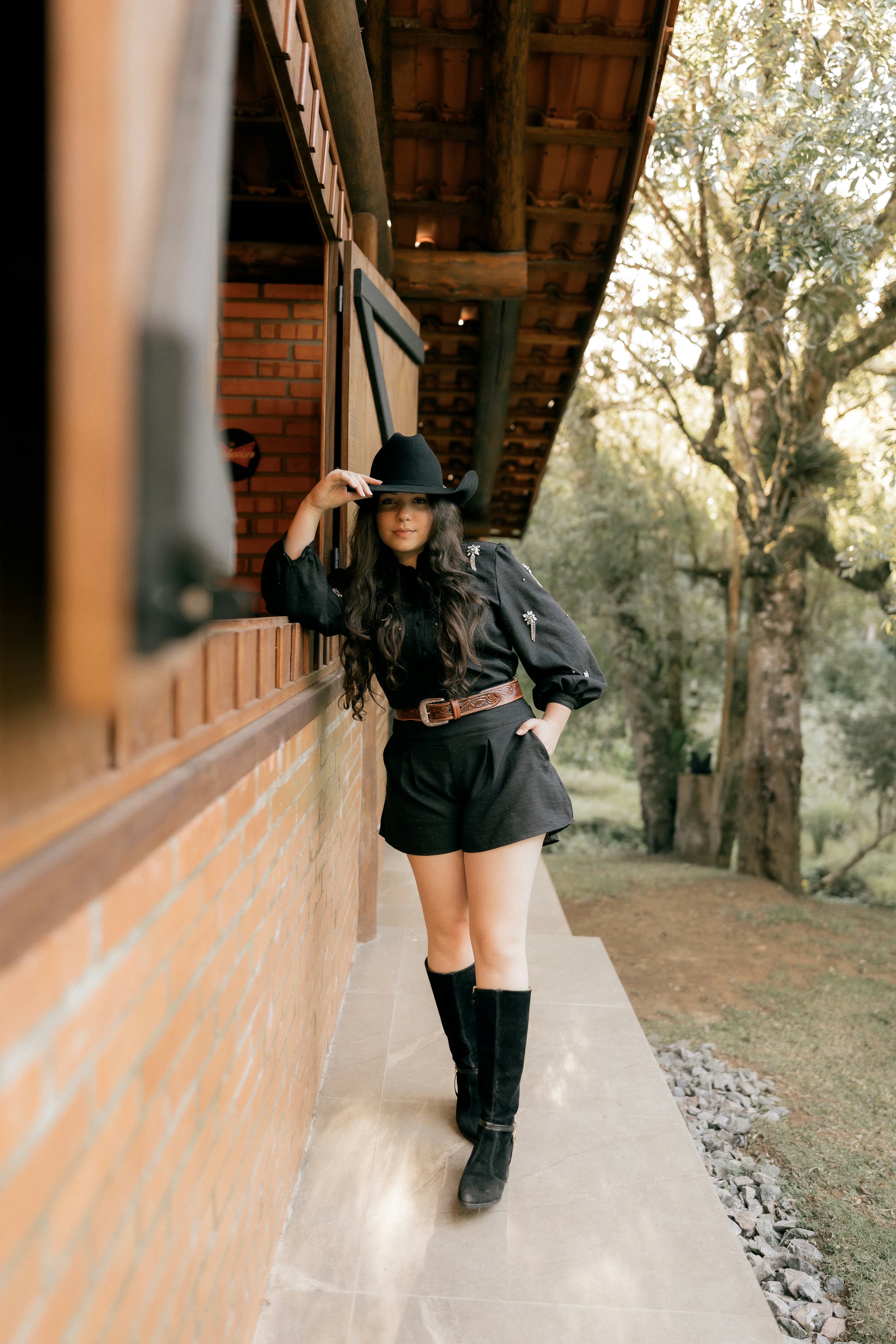 Shadowed Chic: Cowboy Hat Confidence in a Brick-and-Leaf Retreat