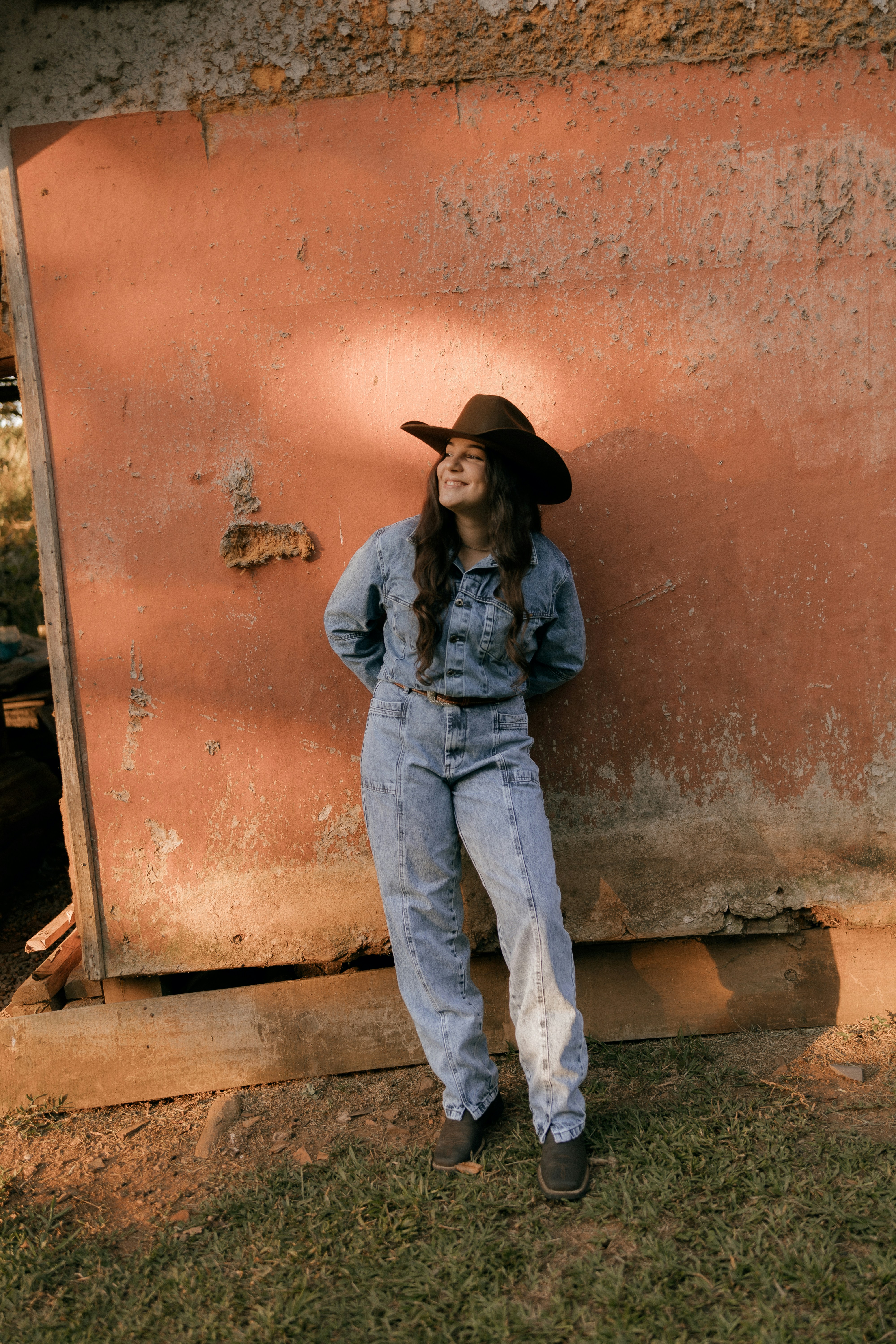 Denim and Derby: A Quiet Portrait by the Sunlit Wall