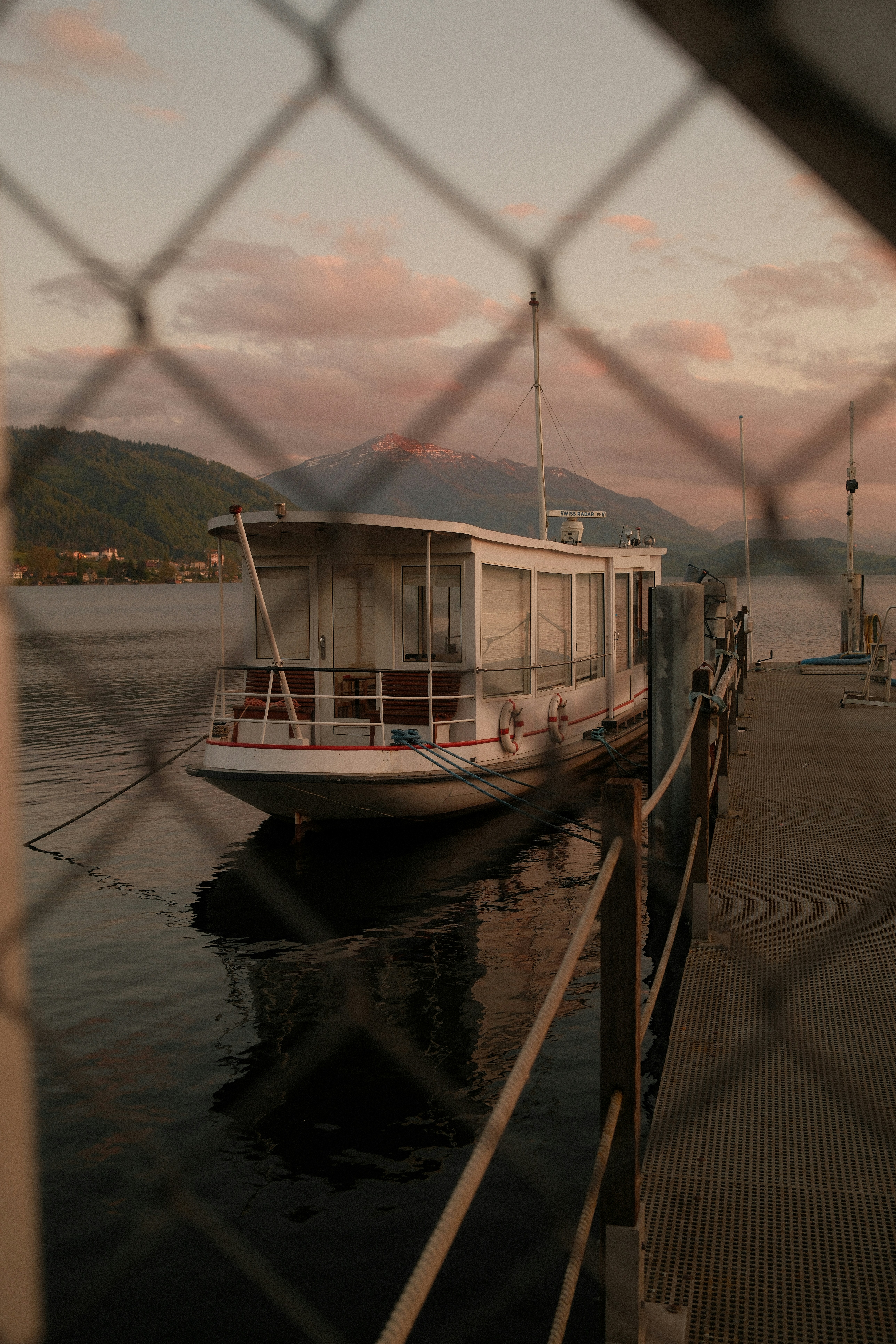 Harbor Vessel Framed by Chain-Link Silence at Dusk