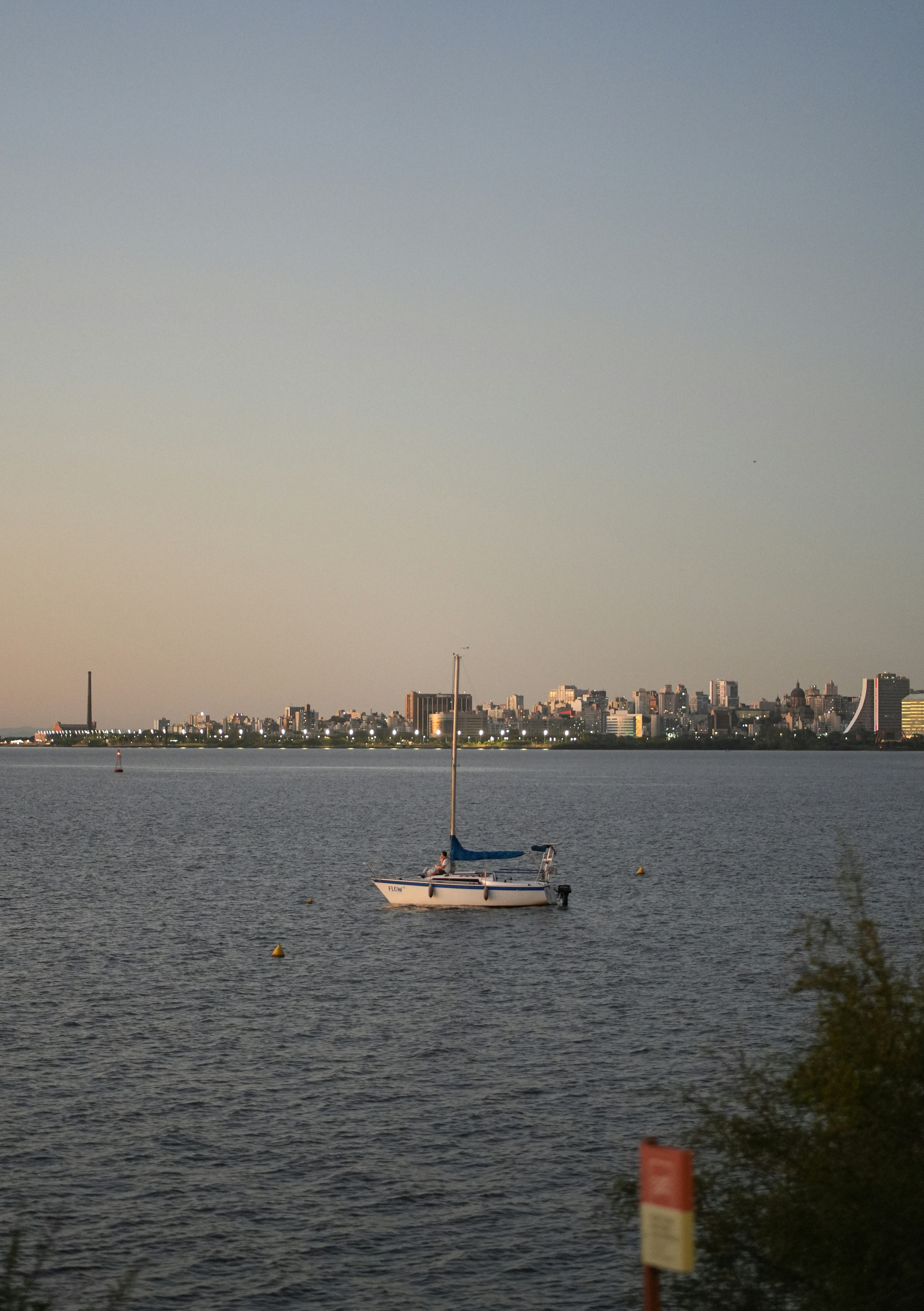 Sailboat in a Quiet Bay at Dusk Over a Calm City Horizon