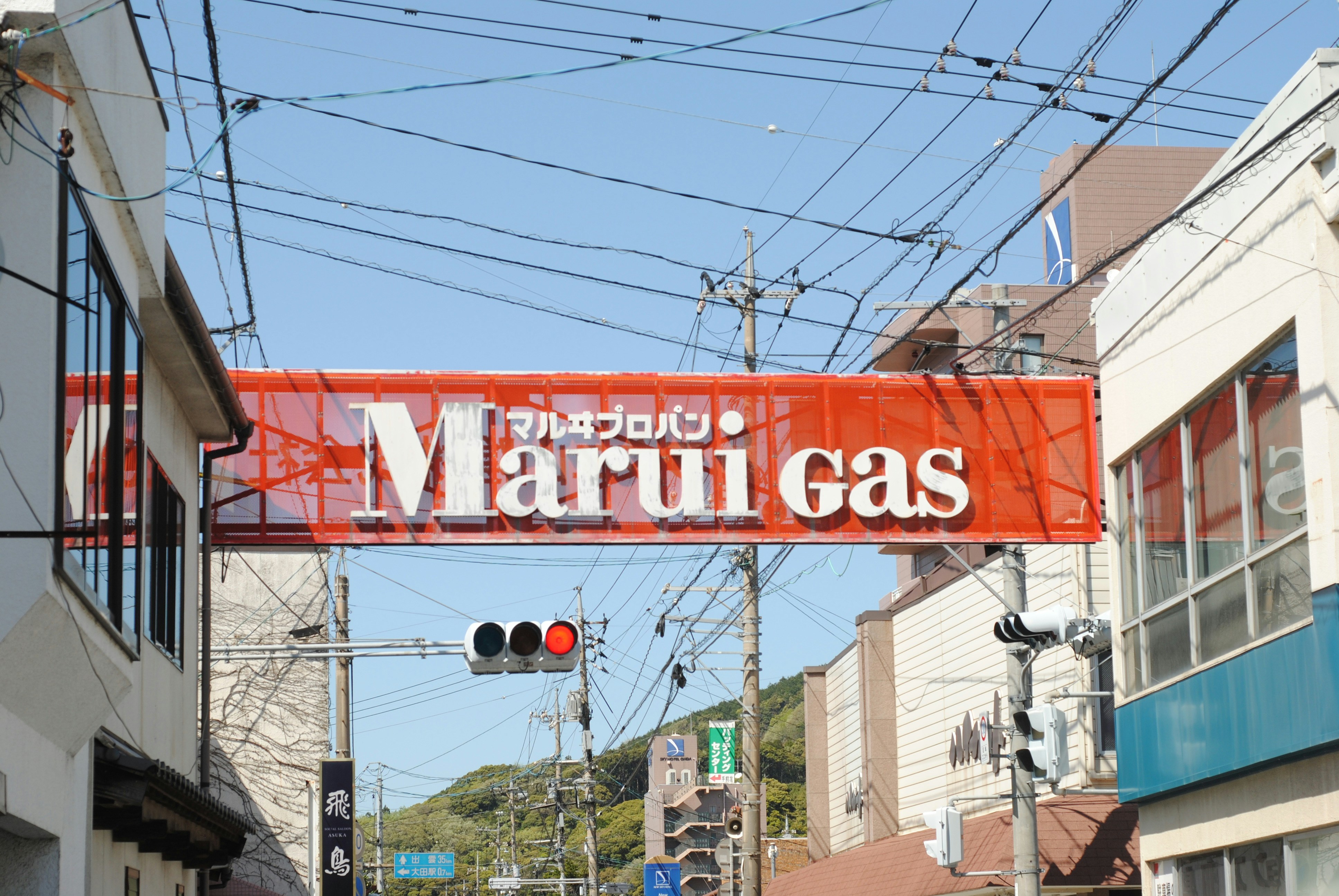 Overhead Marui Gas Banner Spanning a Quiet Japanese Street