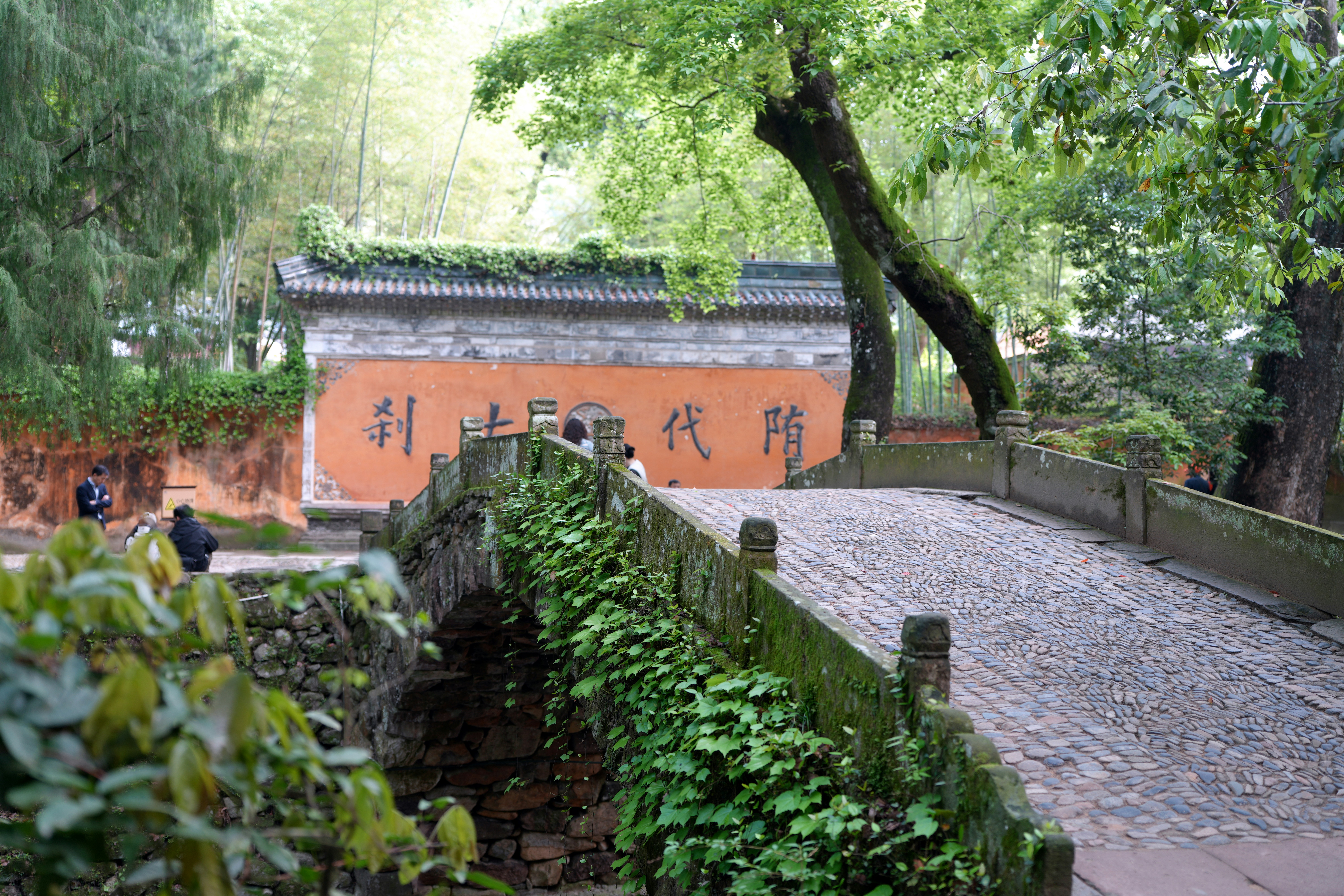 Stone Bridge over Verdant Pathway to a Teal-Top Shrine Wall