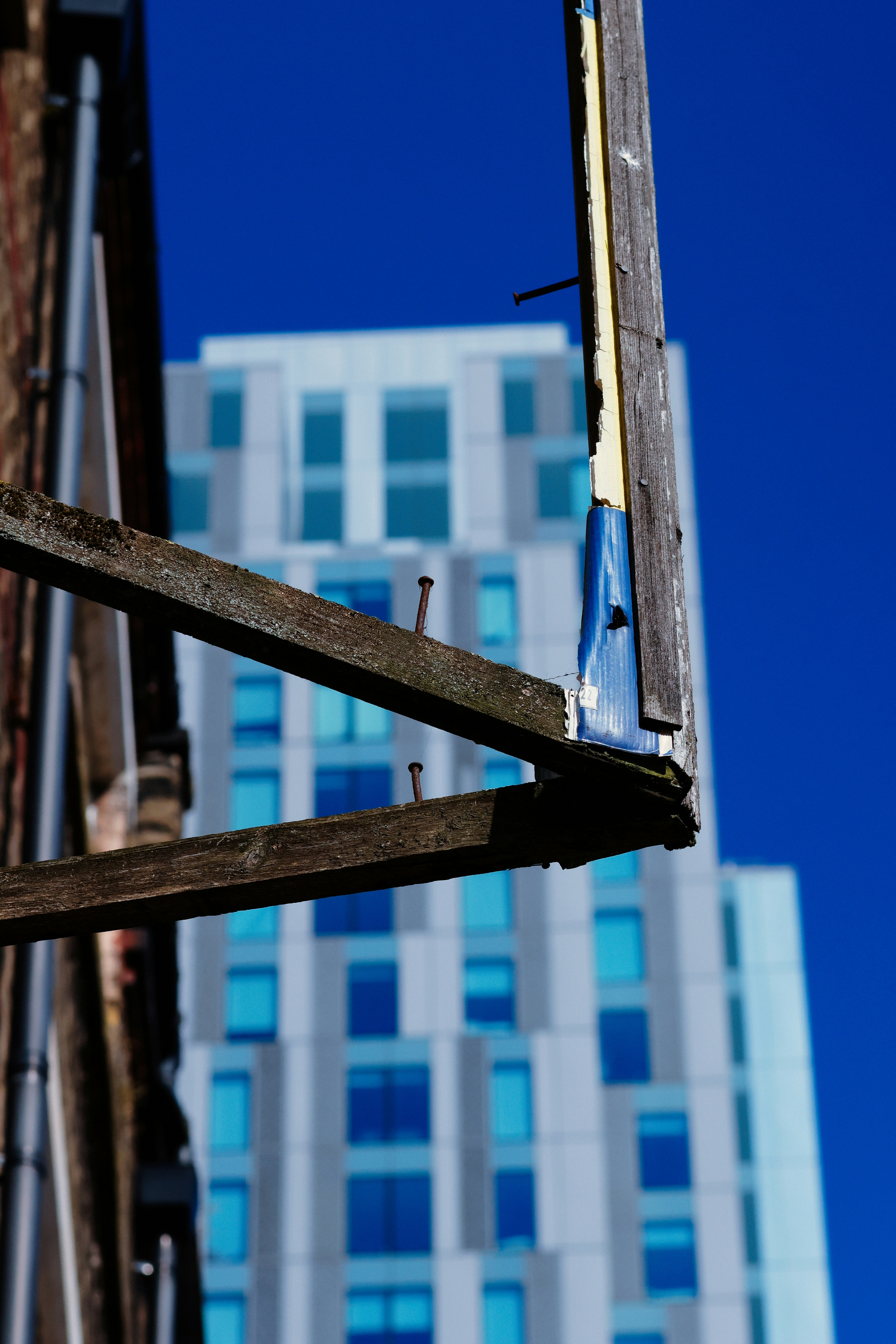 Rusted scaffold in front of a glassed tower under a cobalt sky