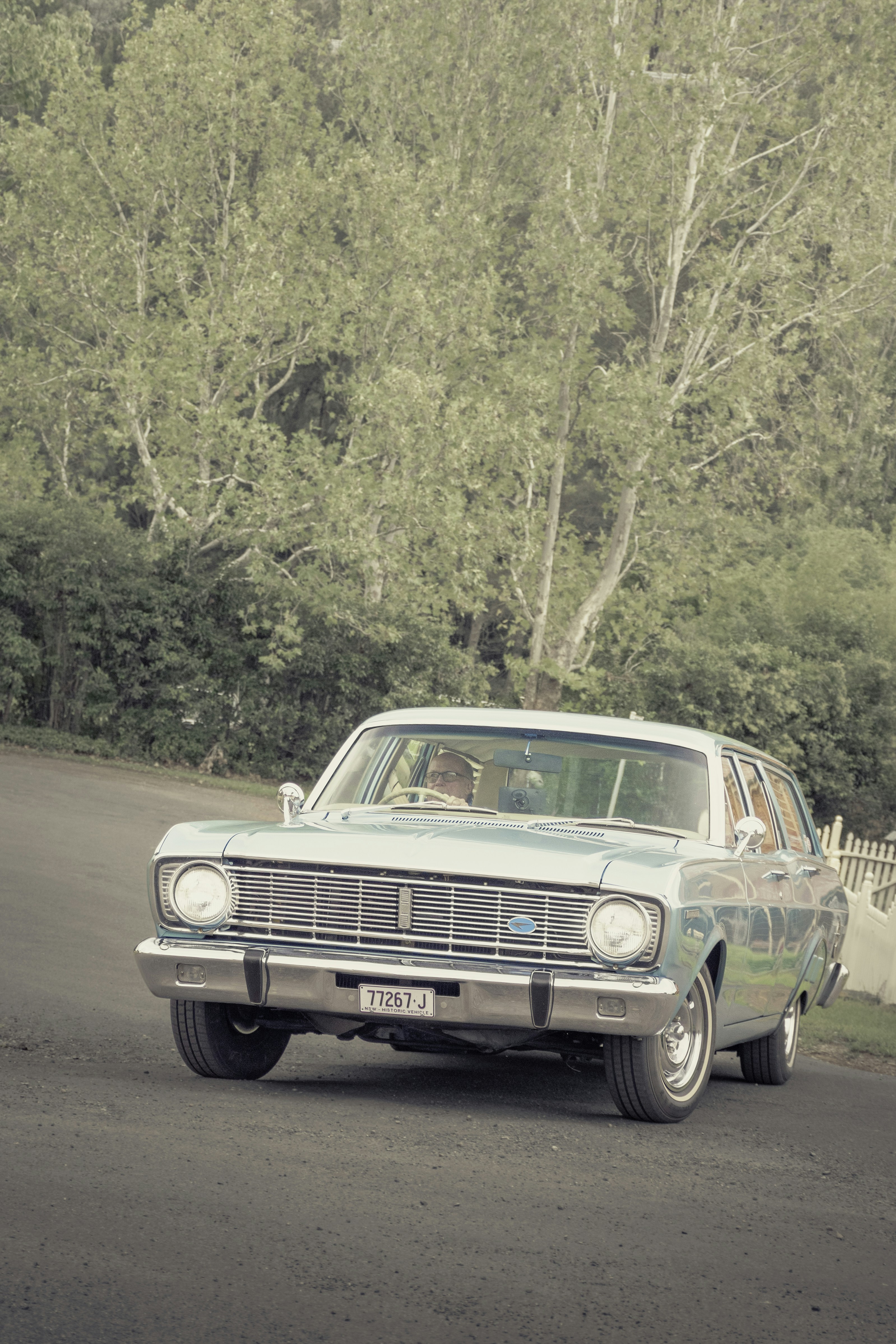 A mint-green vintage sedan corners the road under a pale afternoon sky