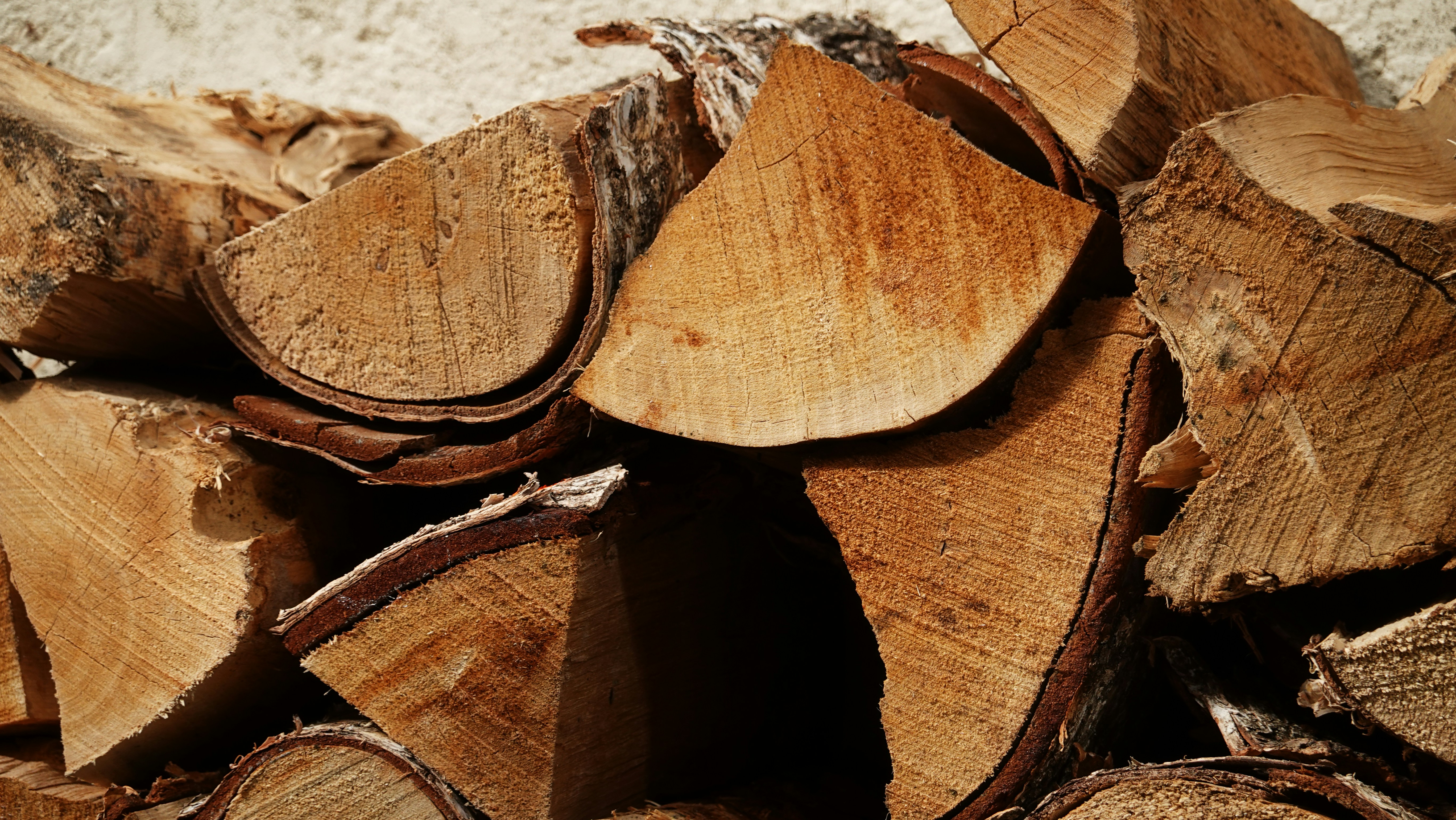 Close-up of stacked firewood with warm tones and pronounced grain forming geometric shapes; the image emphasizes texture and woodcut-like slices.