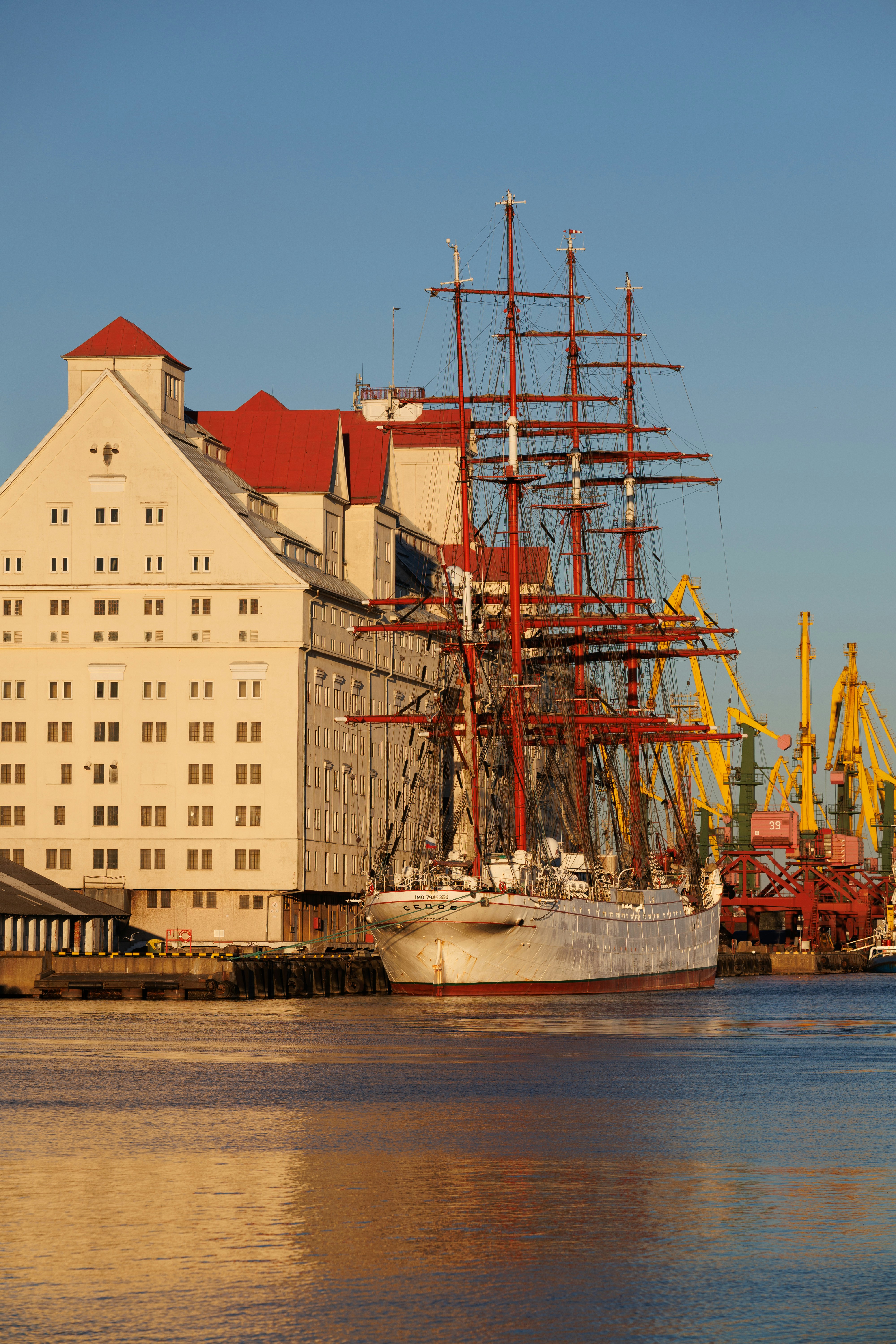Tall ships at the quay: a harbor portrait with red rigging and industrial cranes