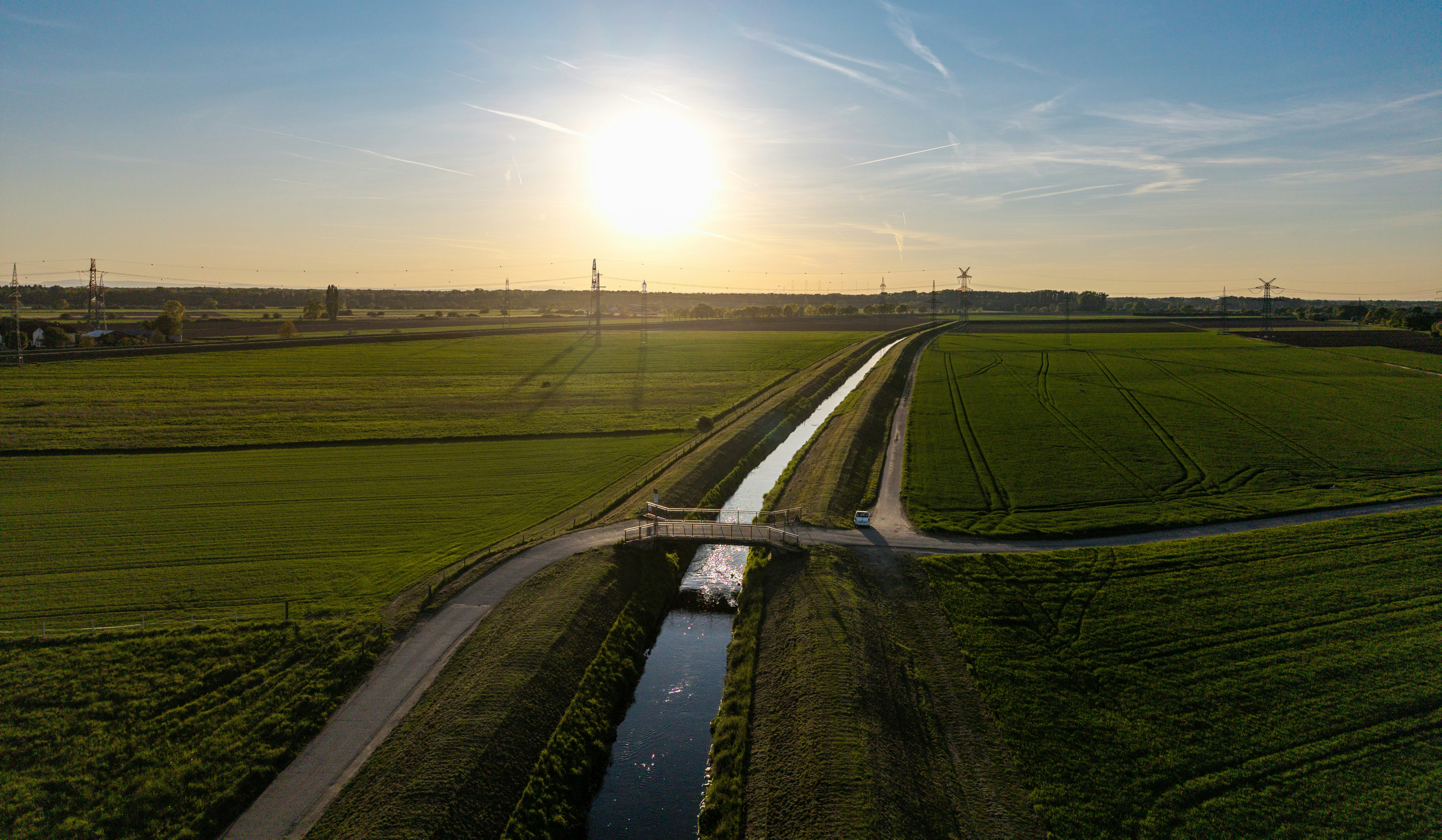 Sunlit Ditch Danse: Aerial View Over Green Fields