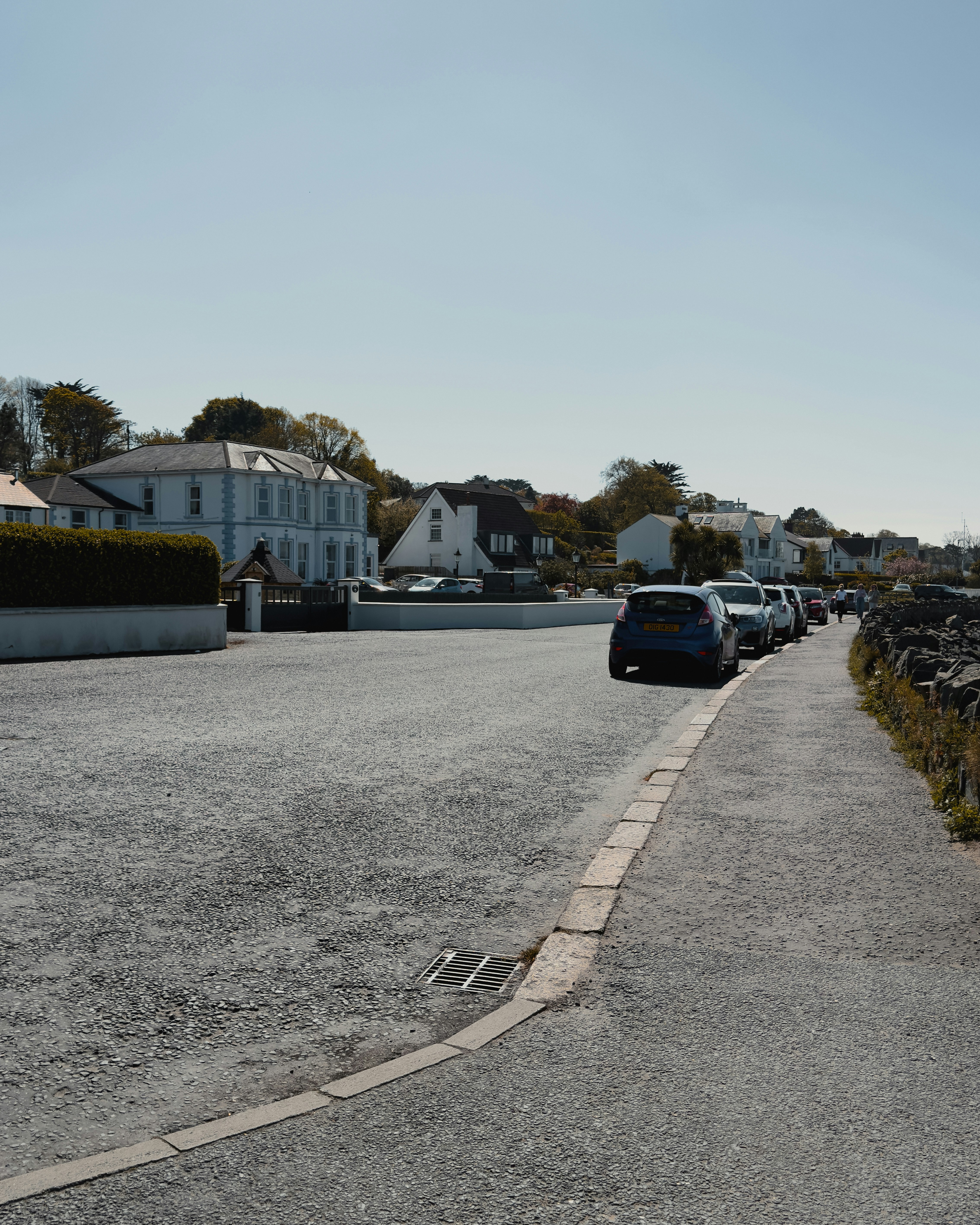 Quiet Coastal Street with Row of Cars and White Houses