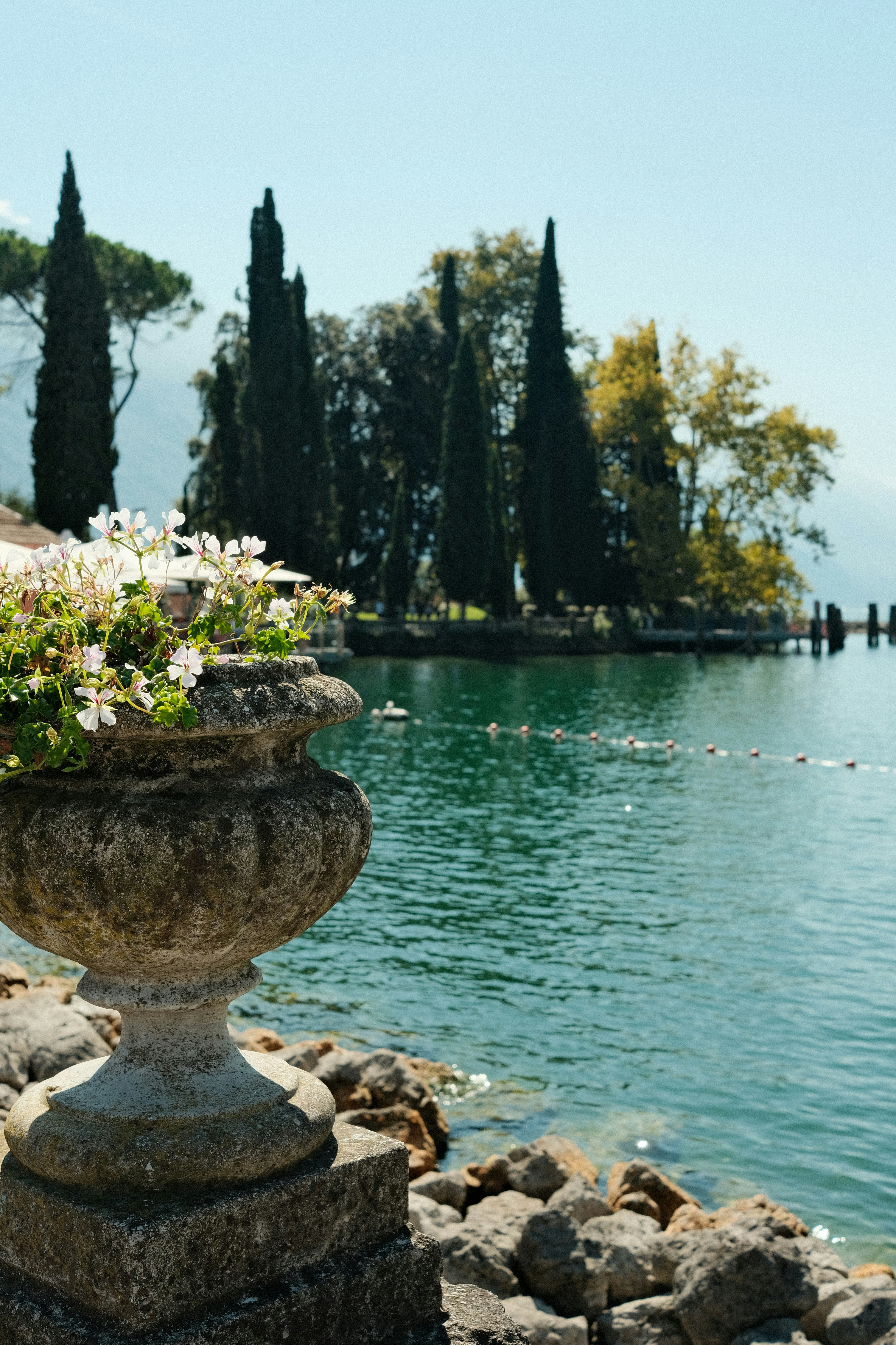 Stone planter with blooming flowers overlooking a tranquil lakeside boulevard