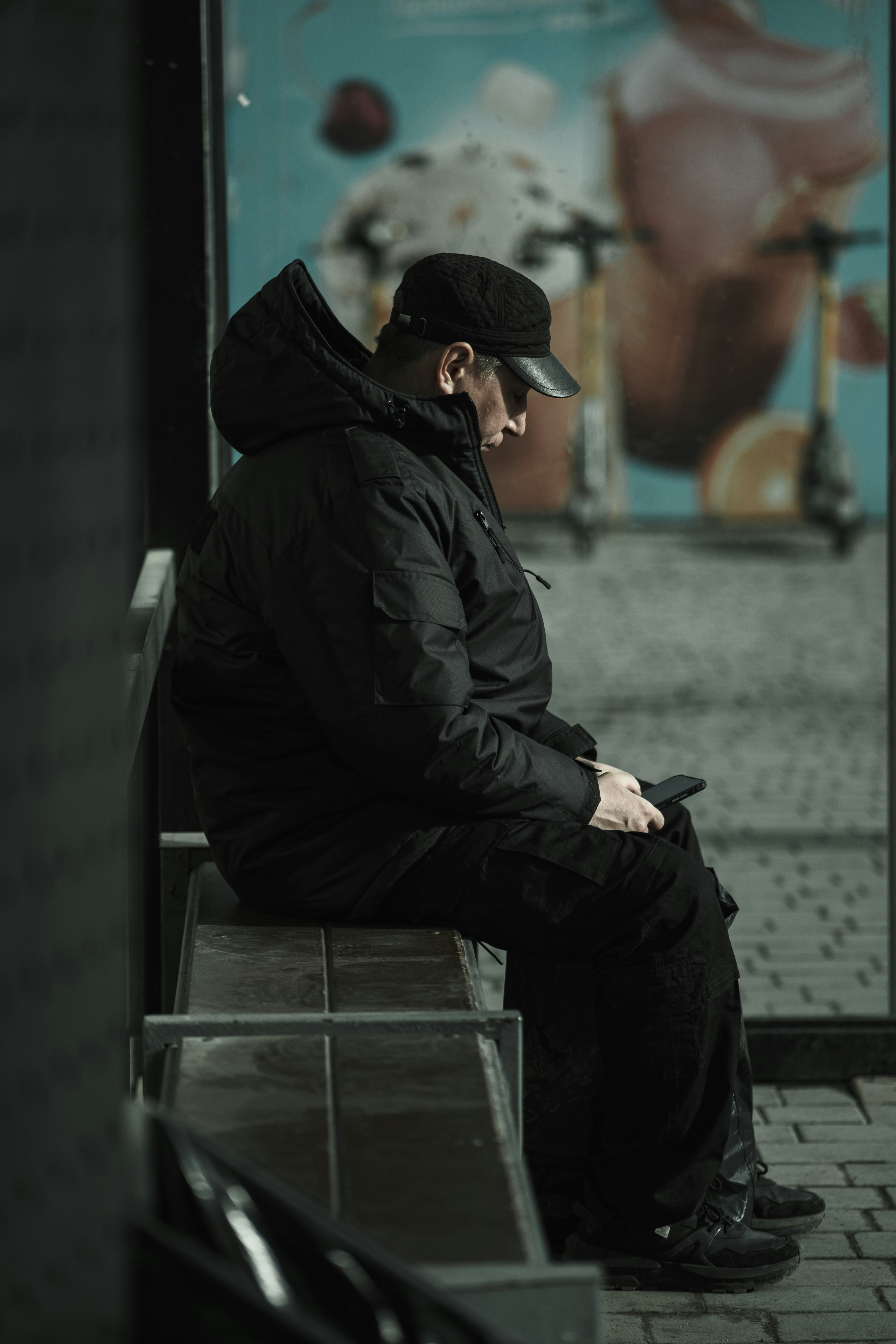 Quiet Pause: A man in black sits absorbed in his device against a mural of cooling treats