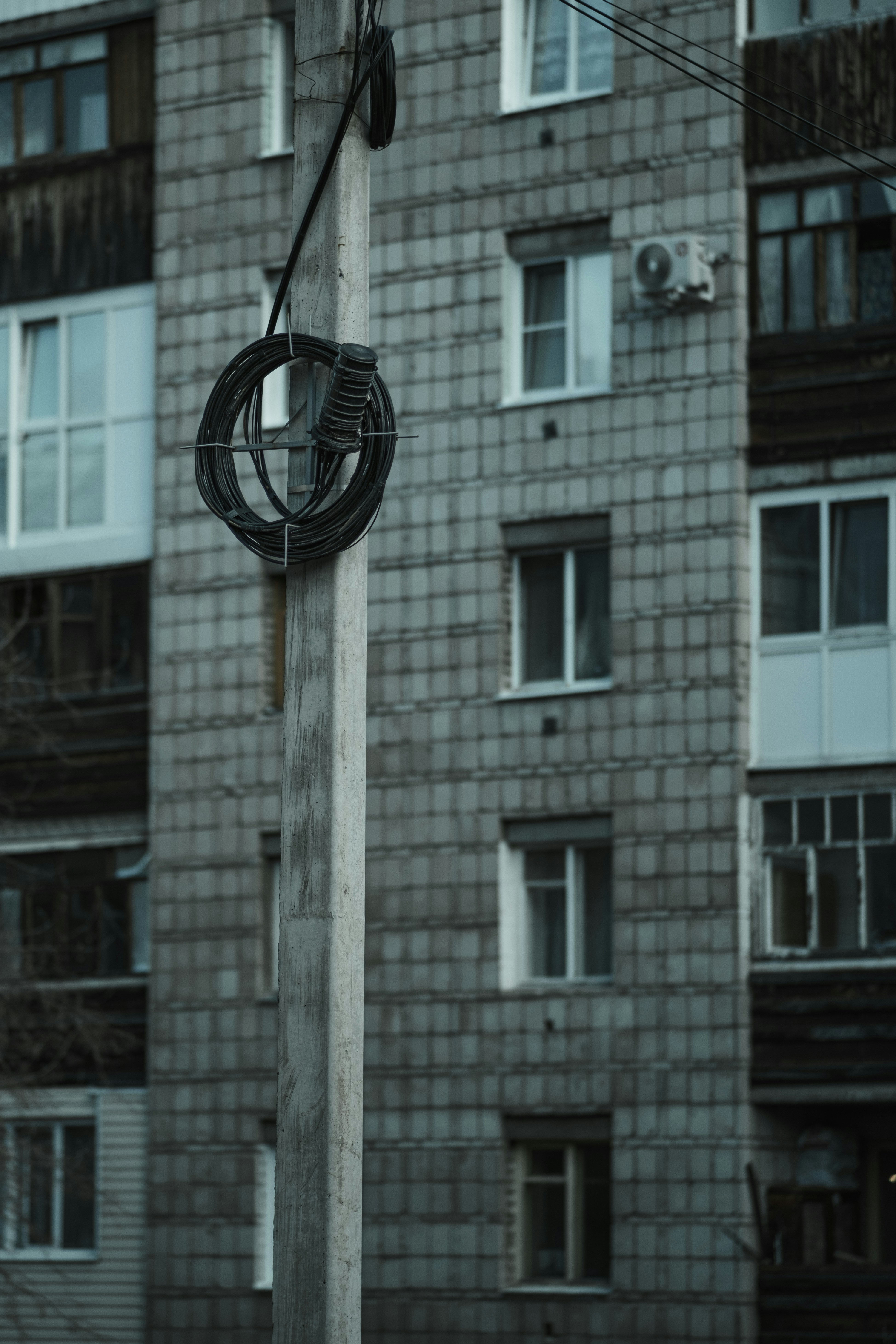 Coiled Cable on a Concrete Pole Against a Distant City Facade