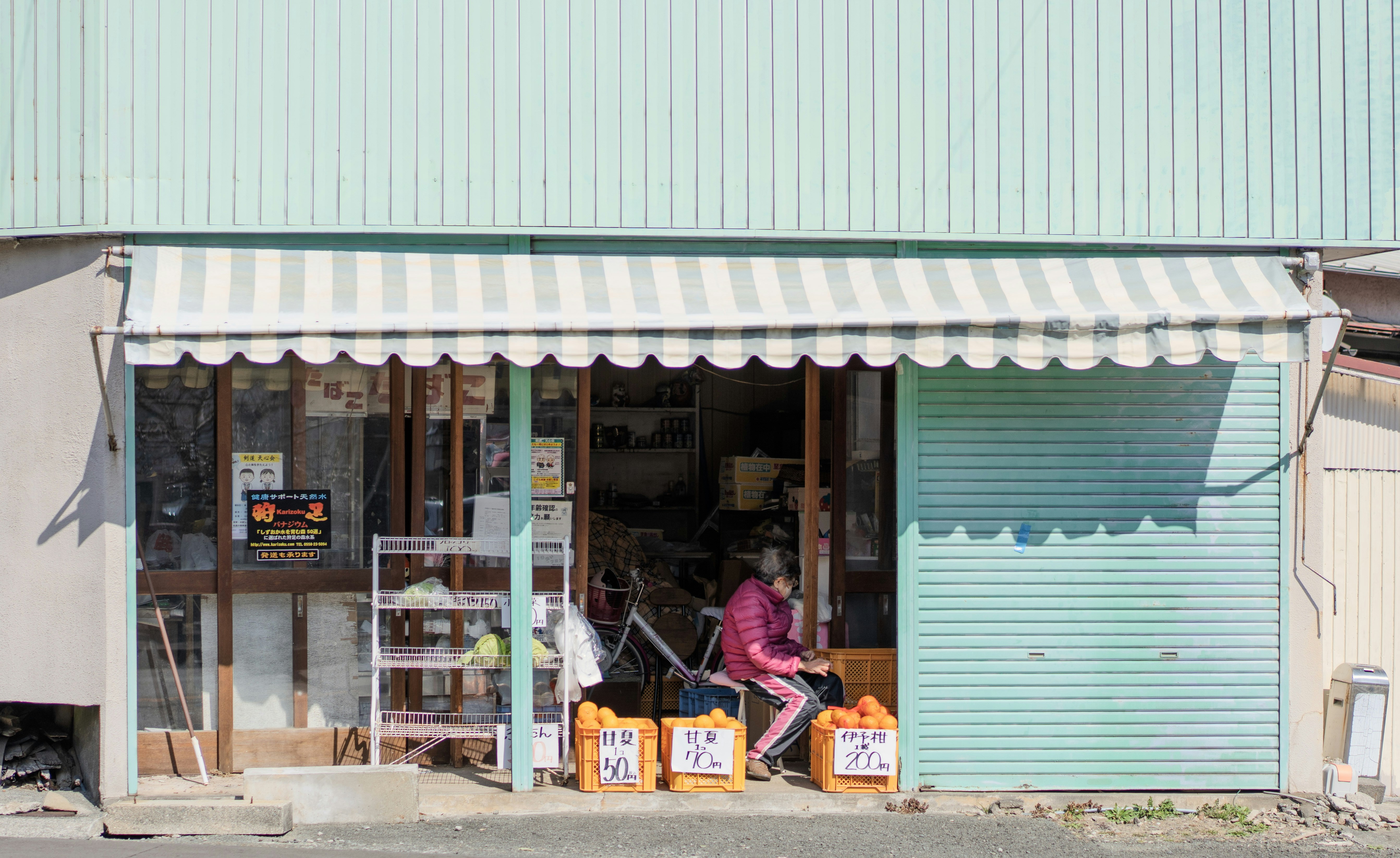 Sunlit Marketfront: A Quiet Street Shop with a Pink-Clad Customer