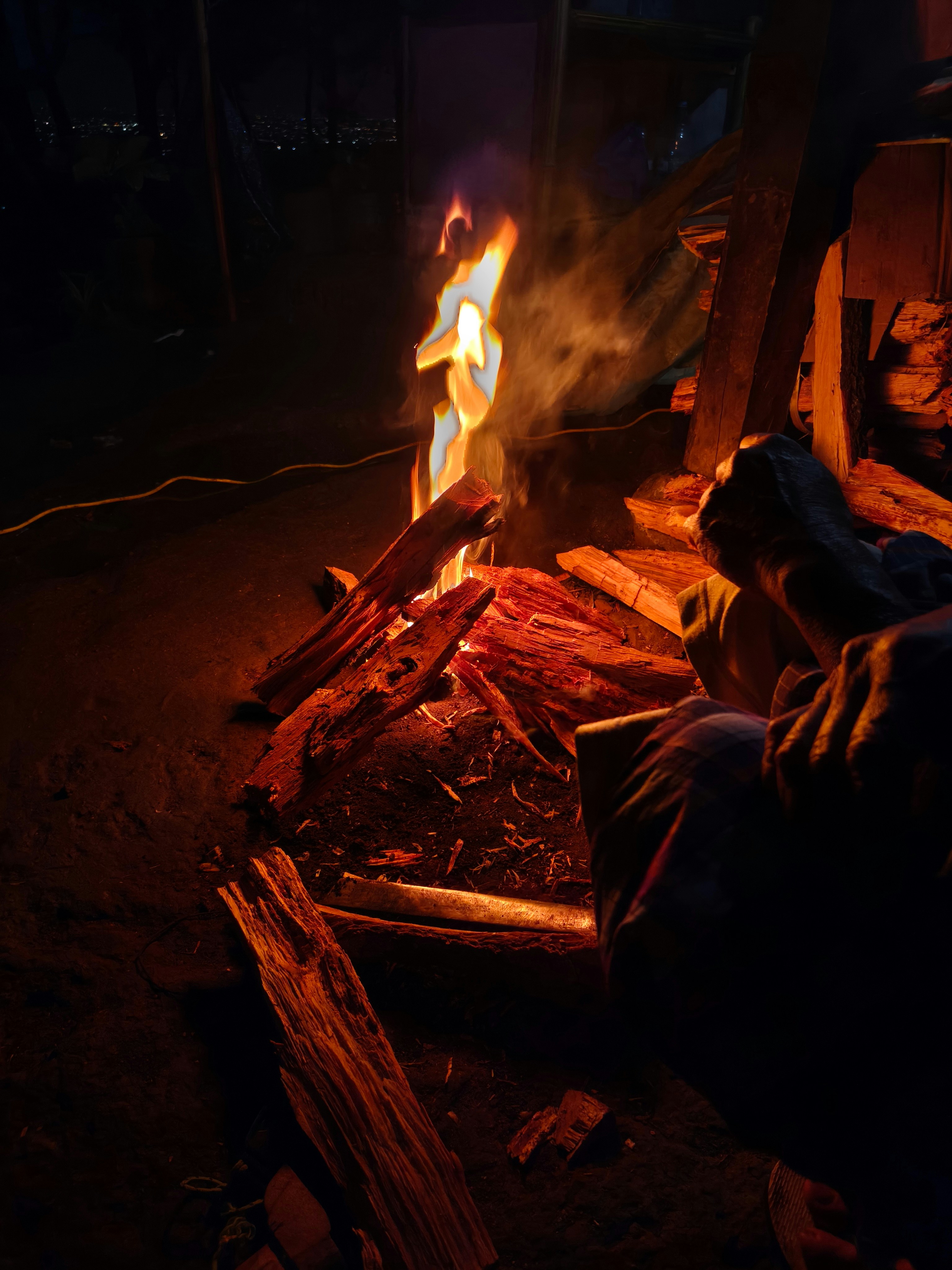 Person sitting by a crackling campfire at night