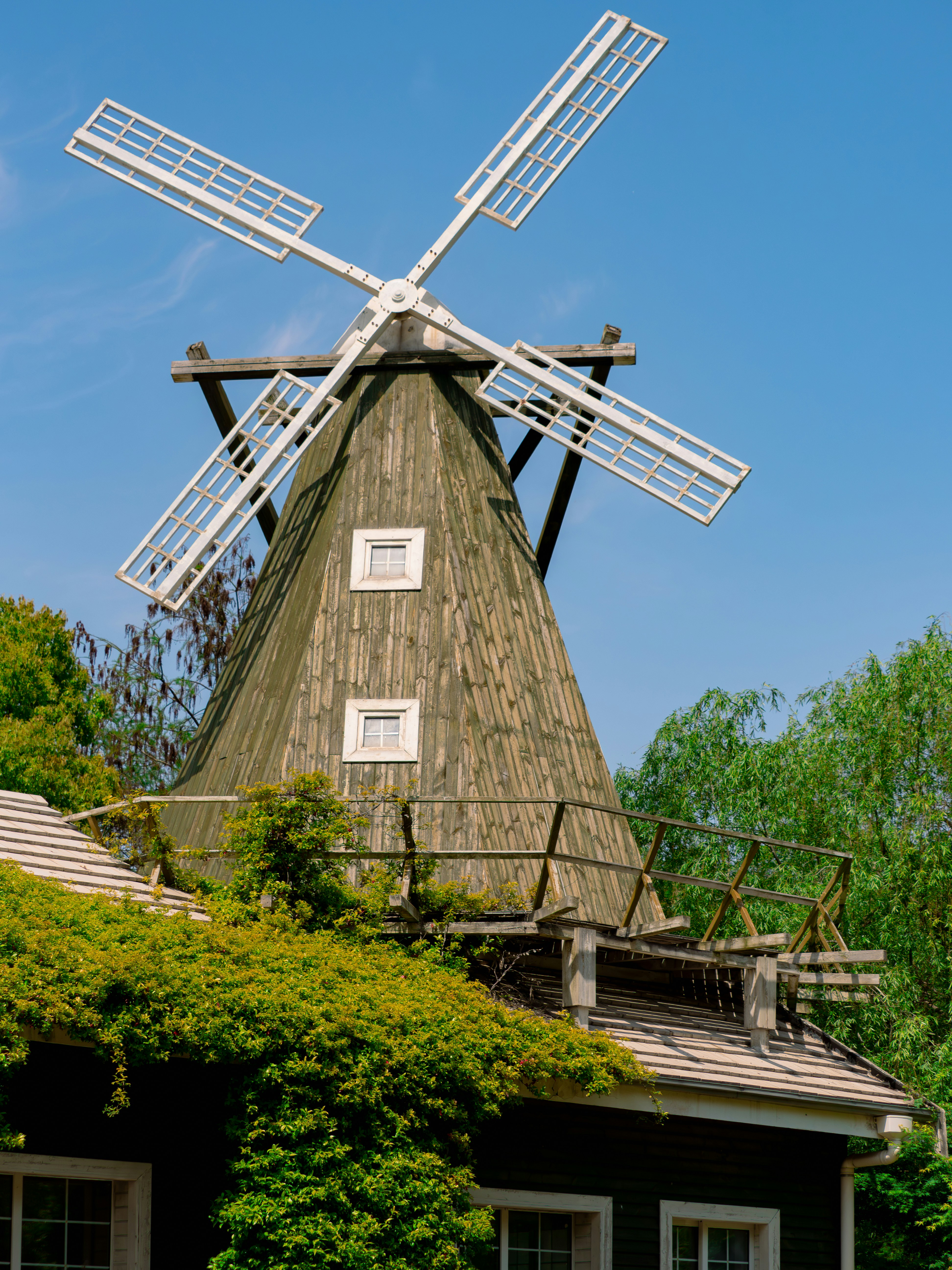 A rustic wooden windmill with white blades against blue sky.