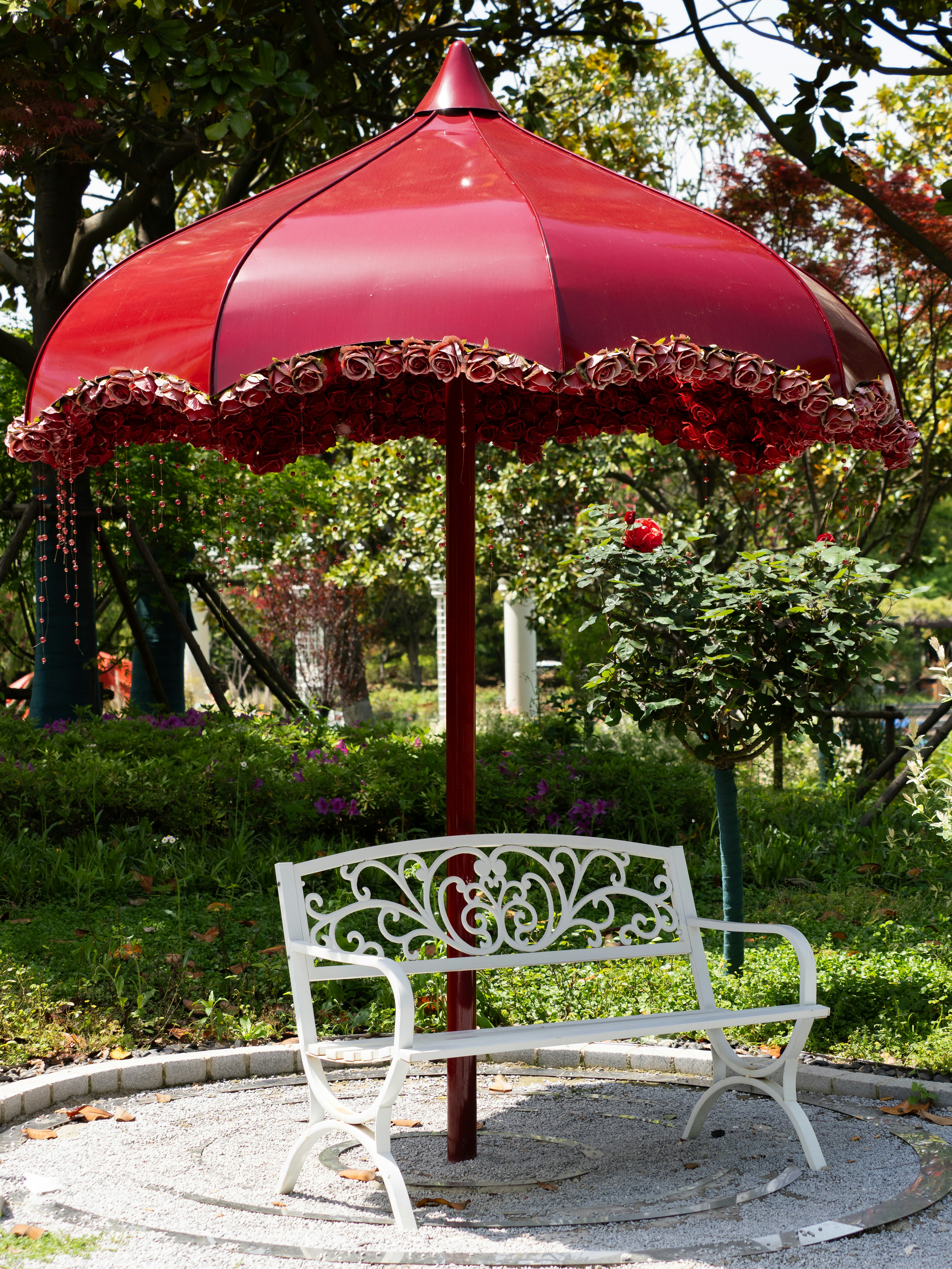 Red Parasol Over a White Ornate Bench in a Quiet Garden