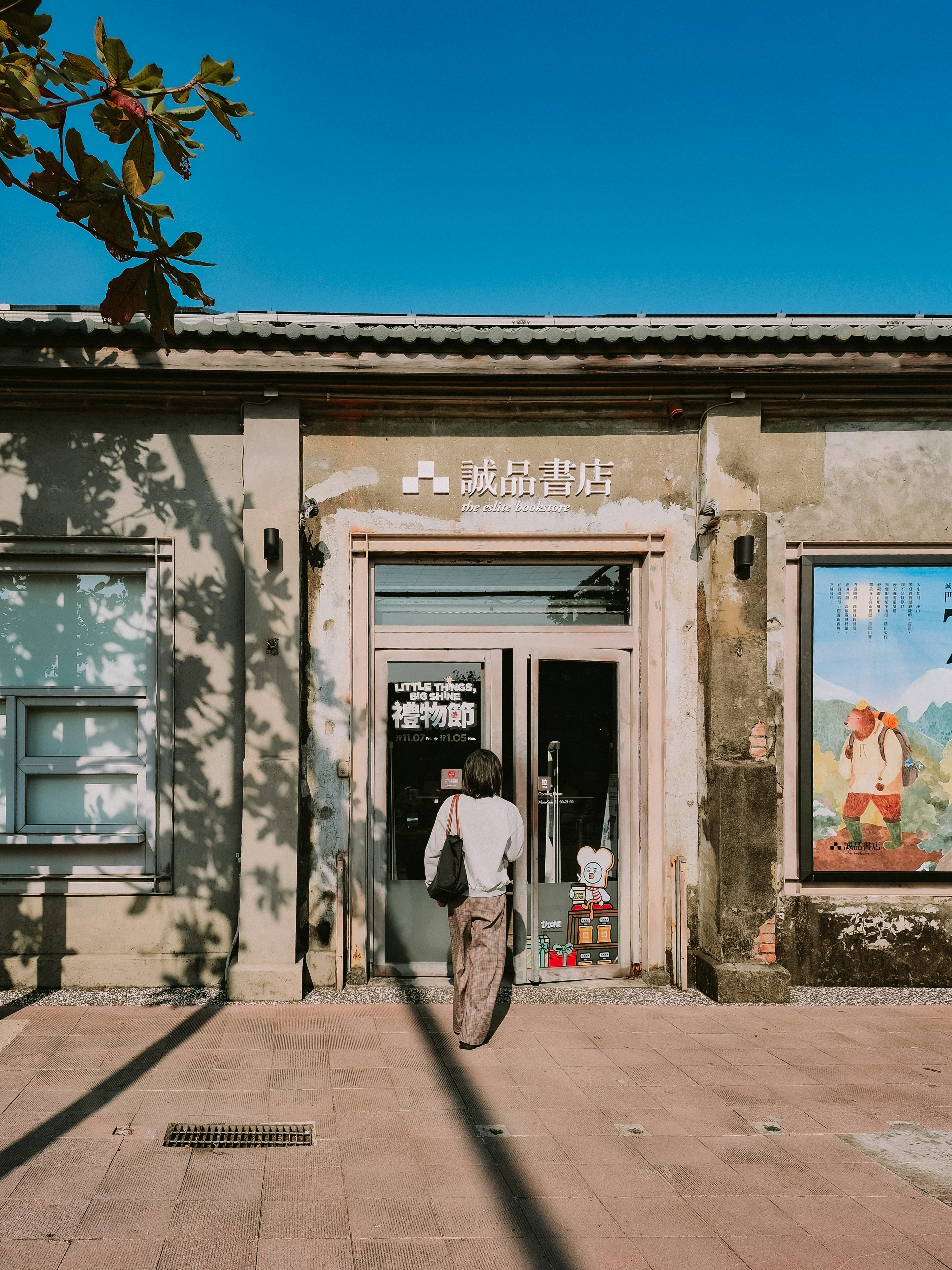 Pedestrian noir at a weathered bookstore doorway under a clear blue sky