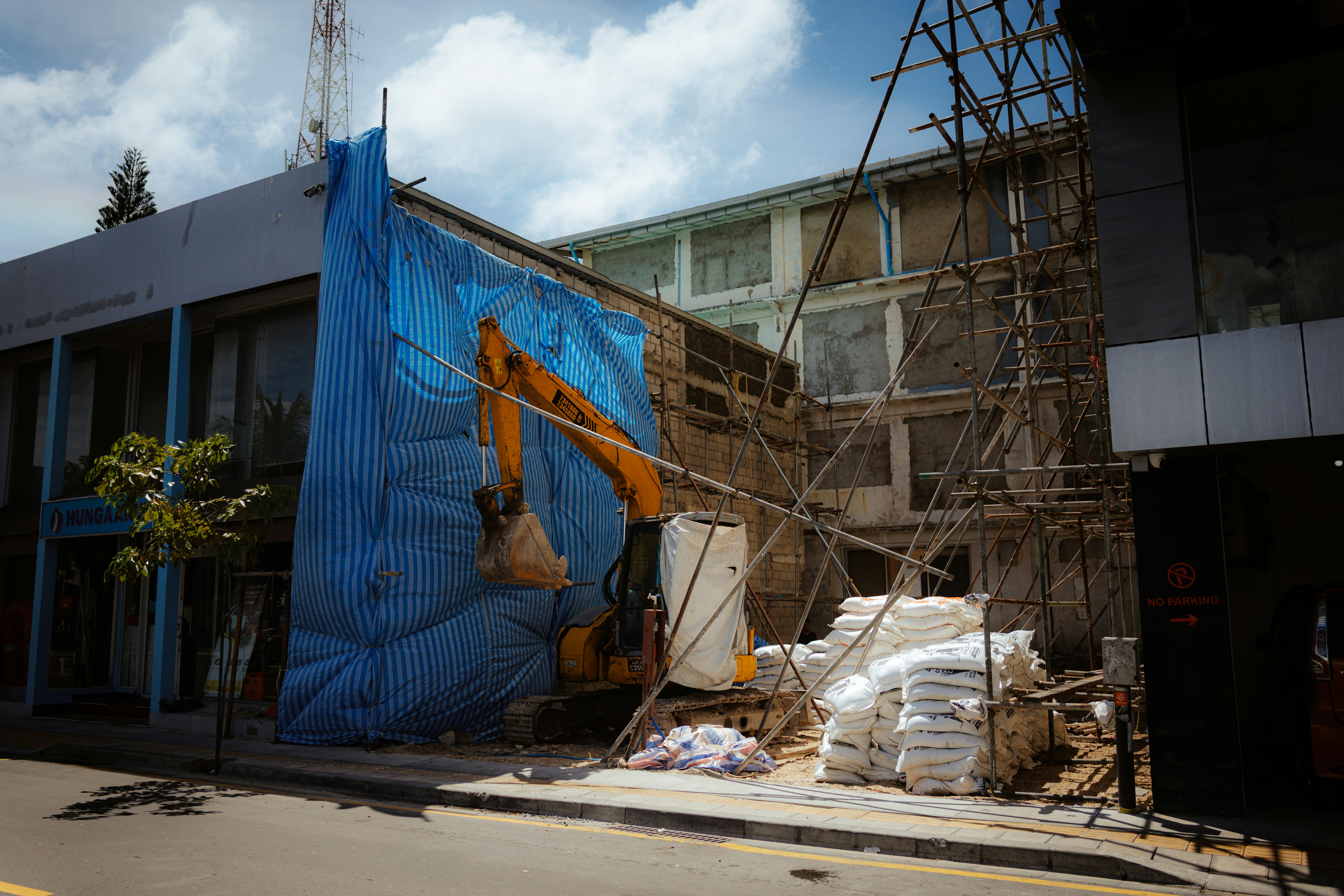 Crane at Work: Blue Tarps and Scaffold Rising Over Building Under Construction