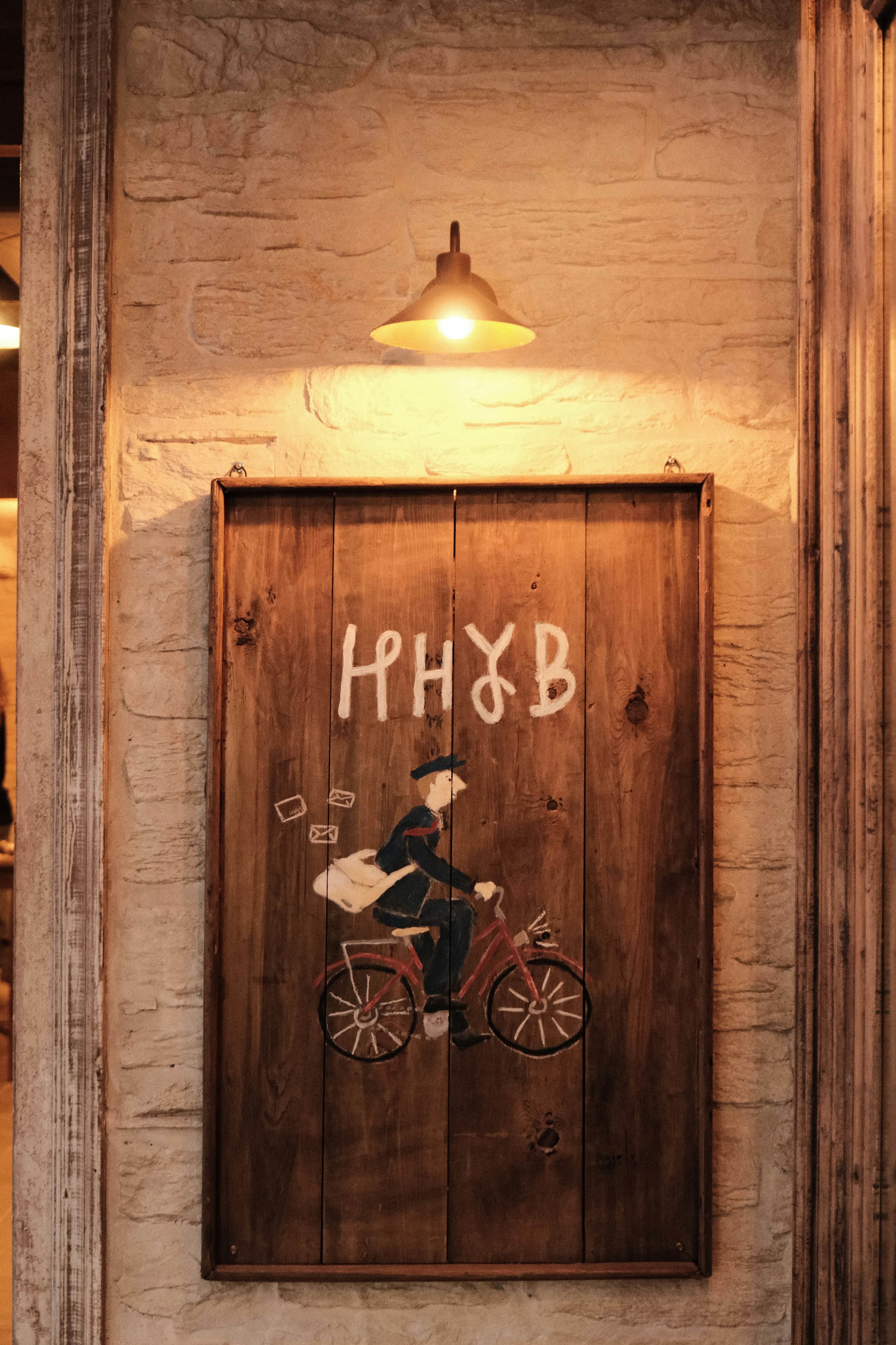 Wooden sign with cyclist and letters under an antique lamp.