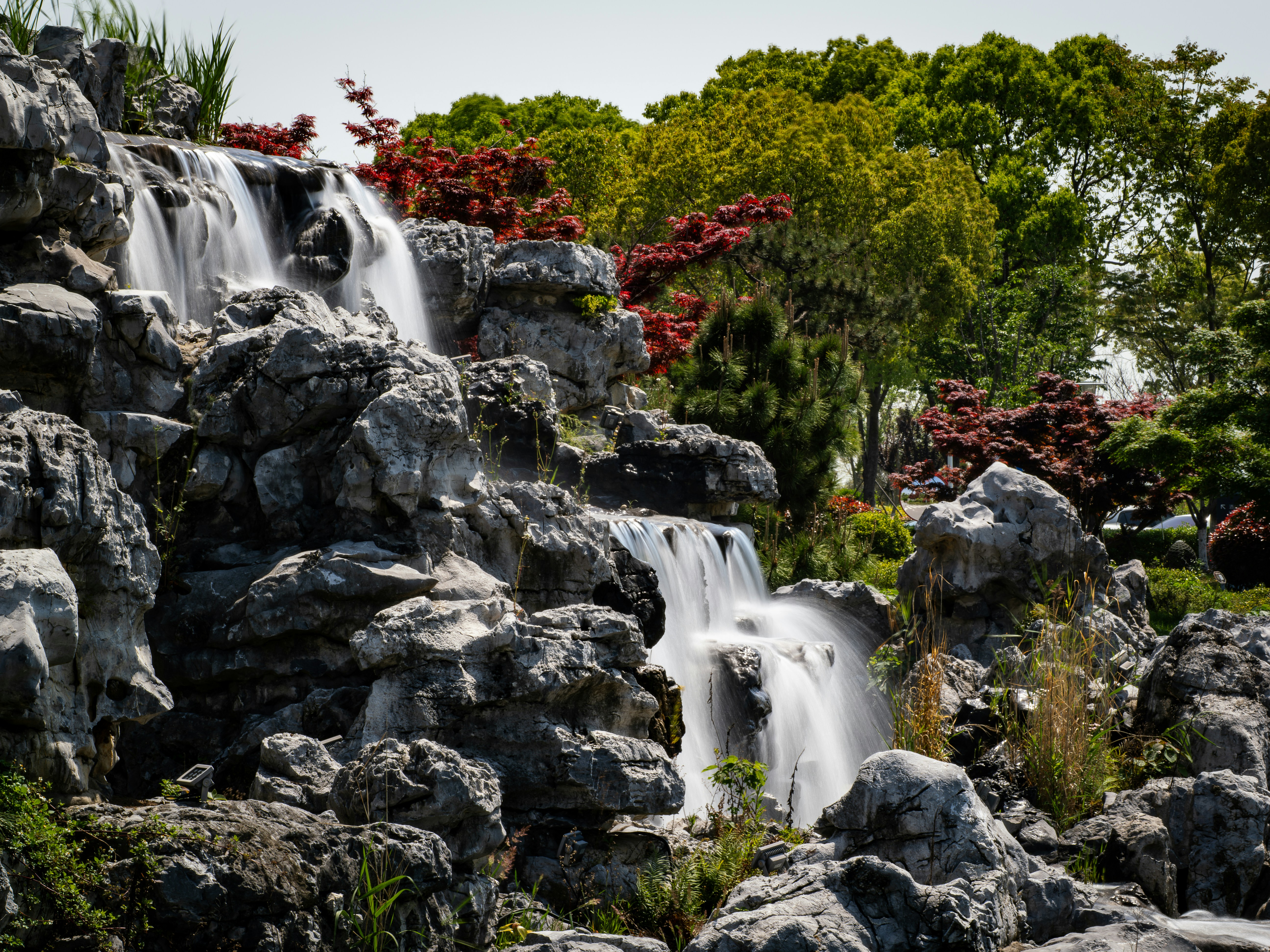 Waterfall composed of rugged stones, framed by autumn-tinted shrubs and a lush green canopy