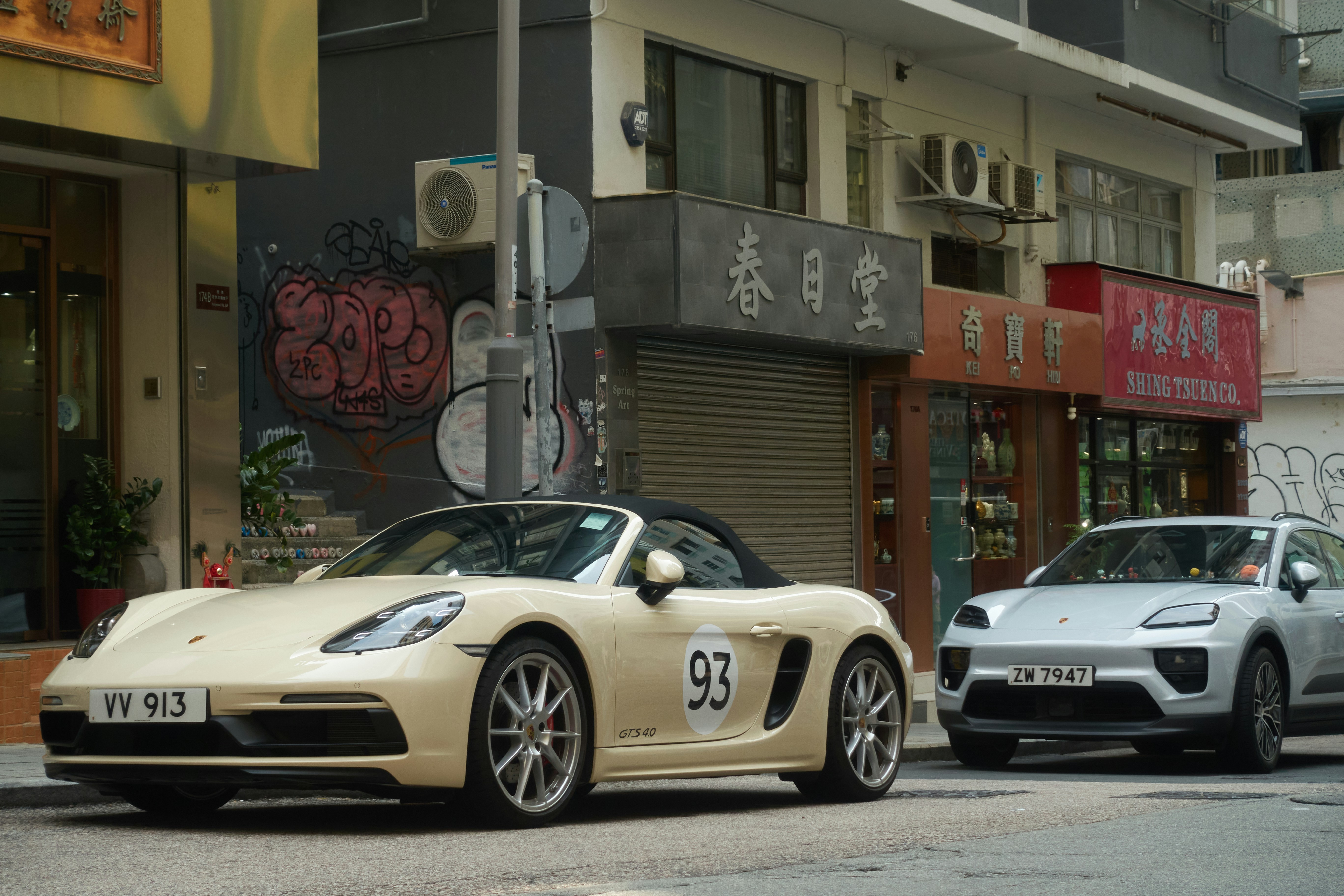 Beige Porsche 718 Spyder and Silver SUV Nestled Along an Urban Street
