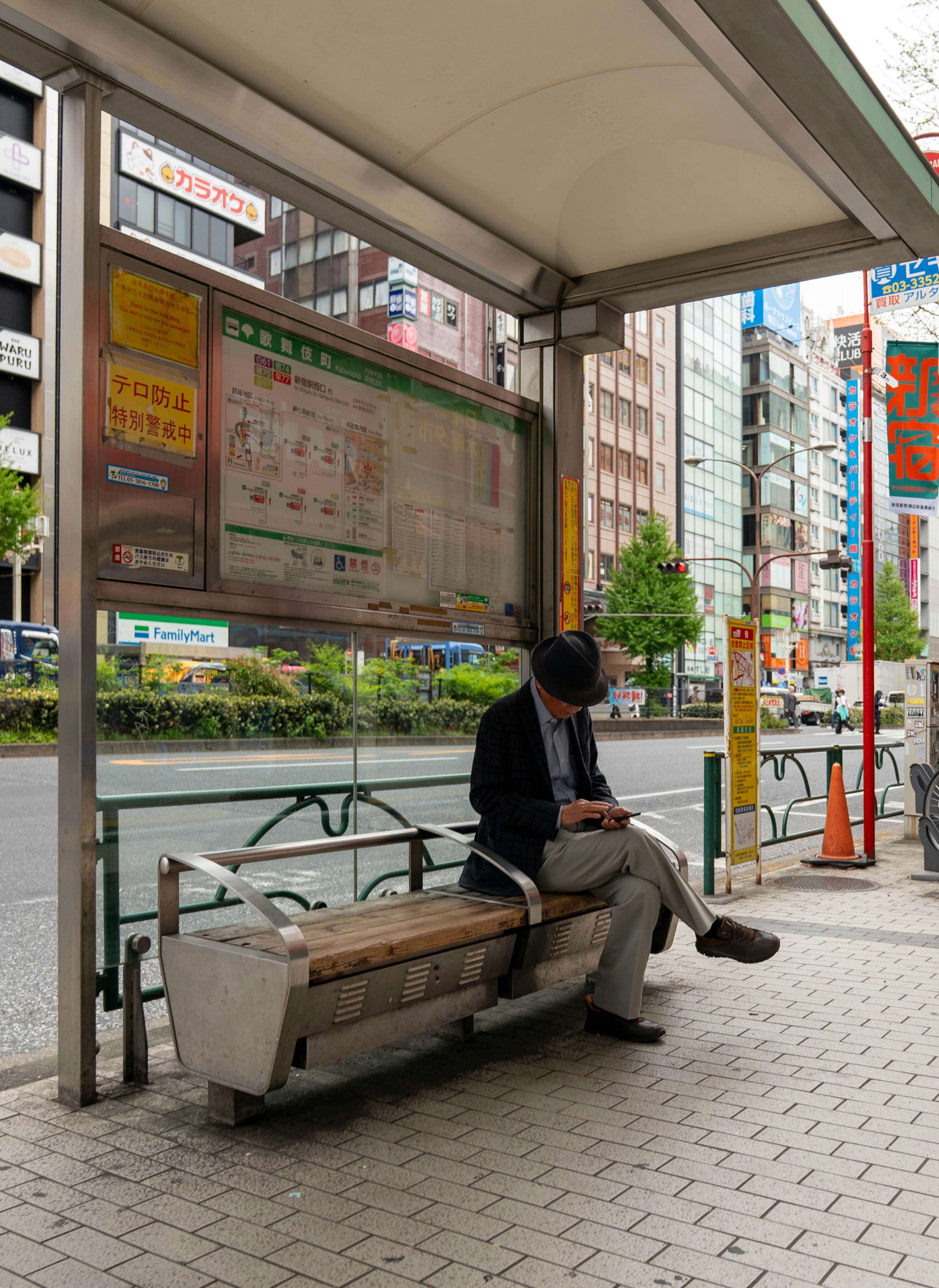 Bus Stop Silence: A man in a hat scrolls through his world