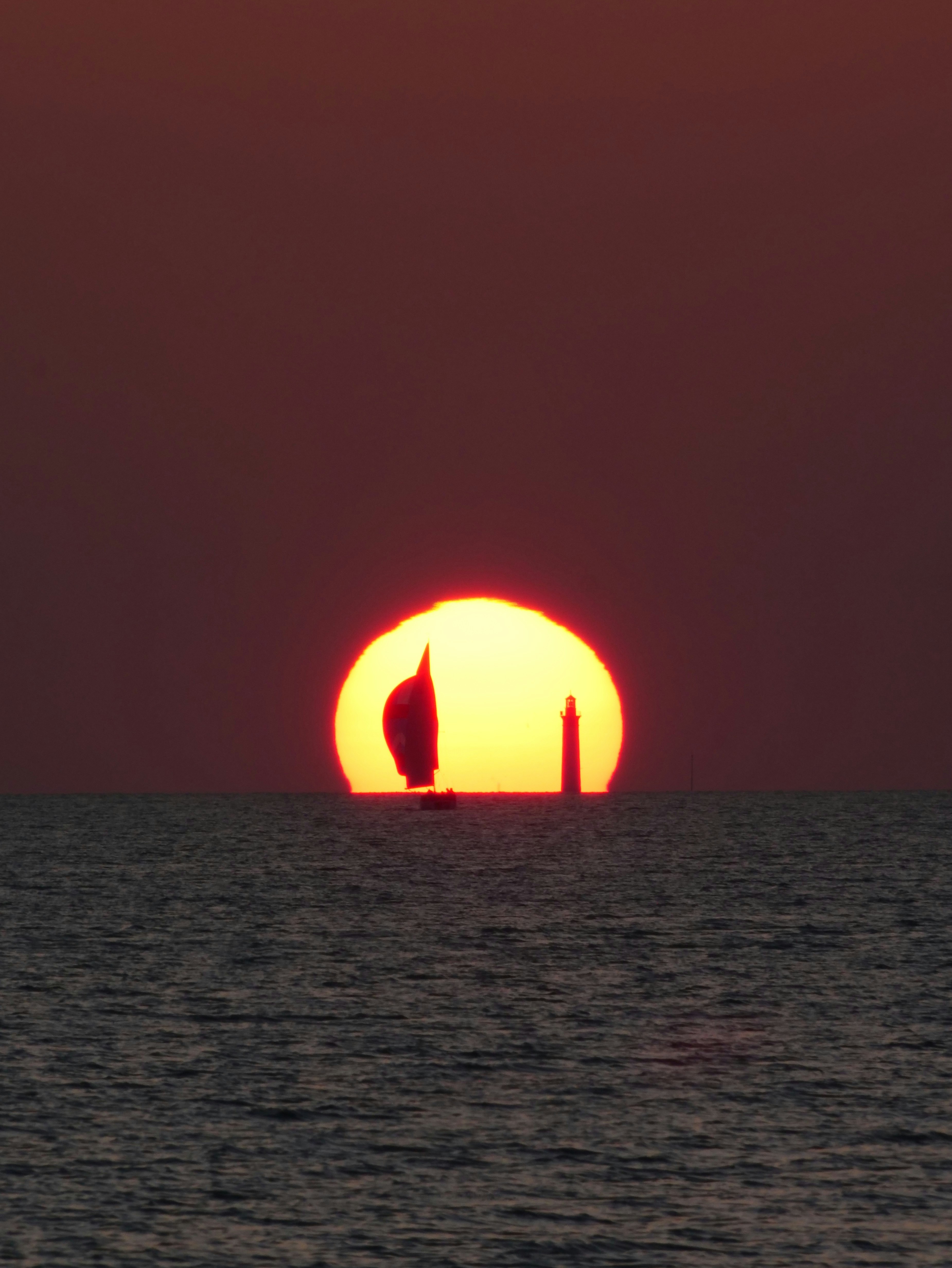 Sunlit Sail at Dusk: A Lone Vessel Silhouetted Against a Flaming Horizon