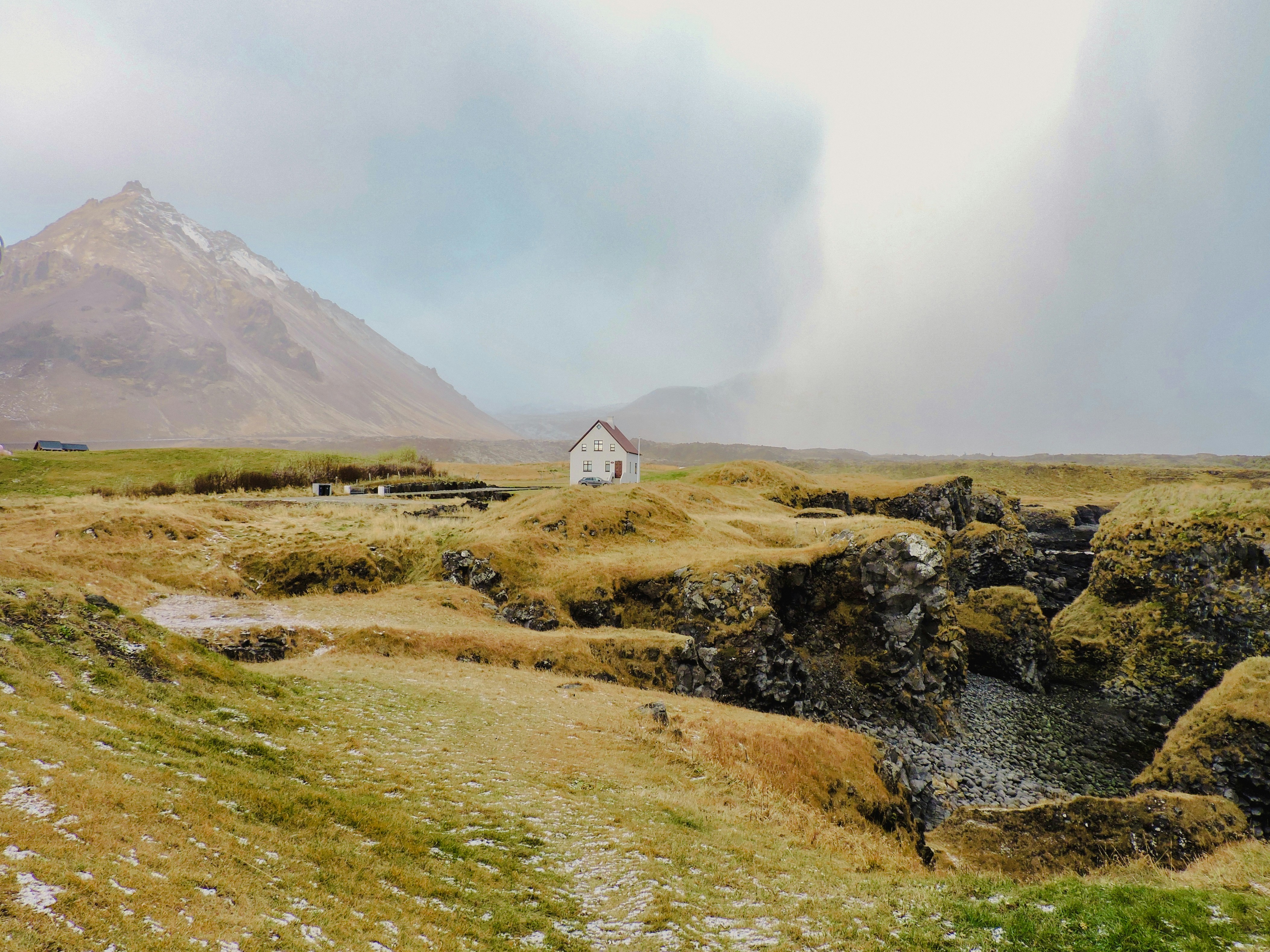 A lone white house at the edge of a chalky canyon under shifting skies